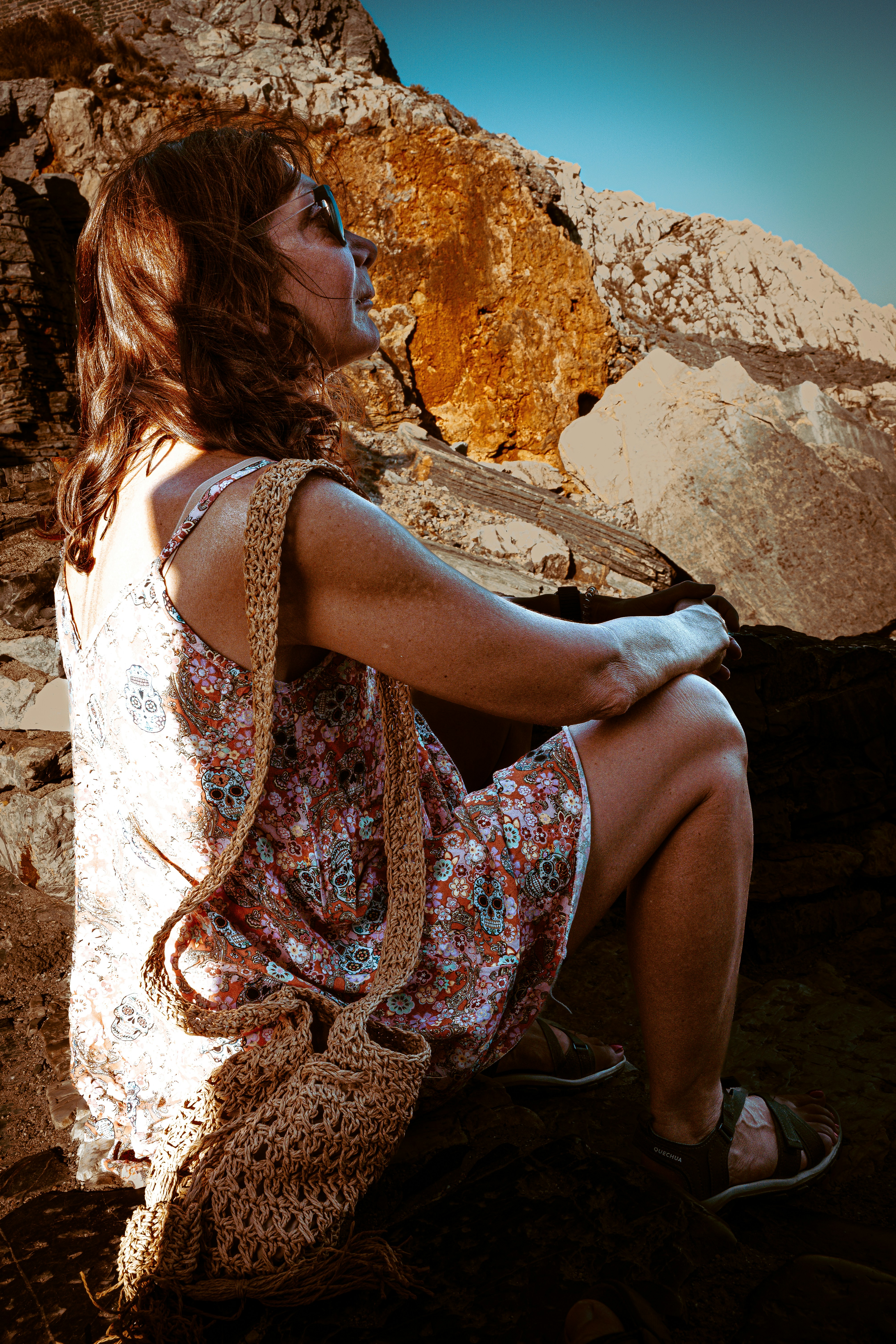 Sunlit Cliffs, Calm Moment: A Woman in Floral Dress Resting by Rugged Coastline