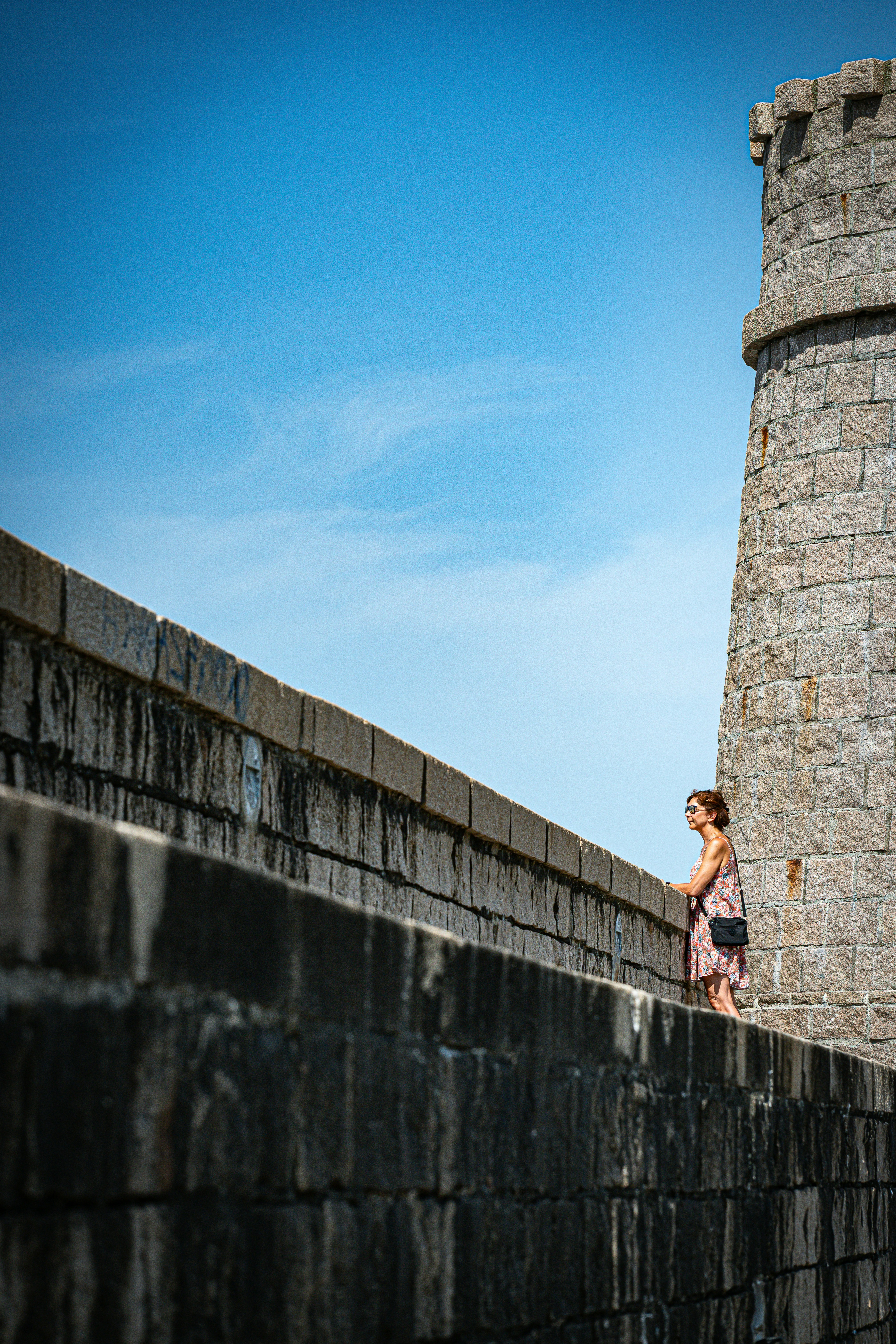 On the Edge: A lone figure at the fortress wall under a wide blue sky