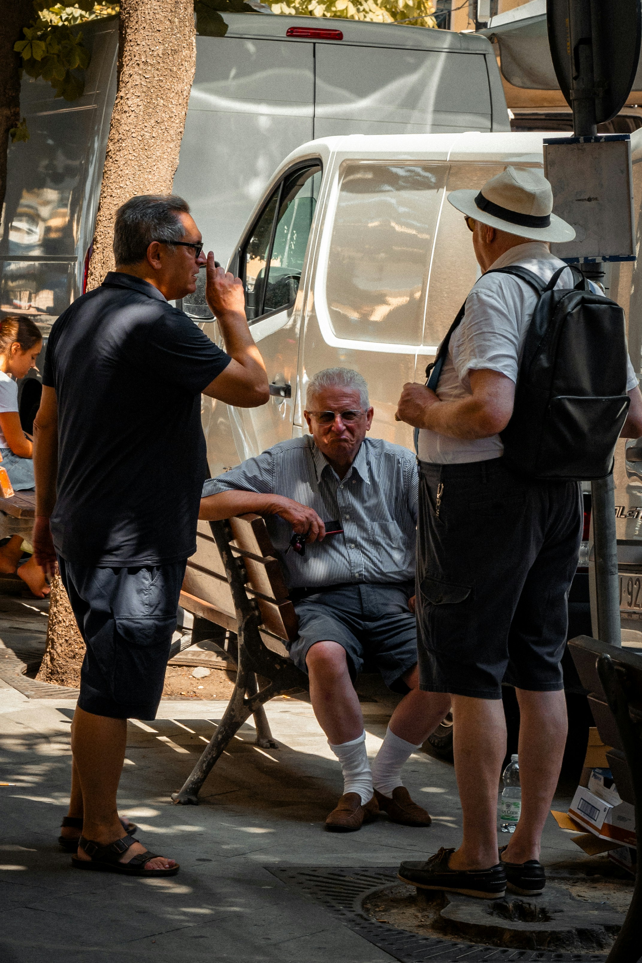 Conversation Under the Van: a group of men in a sunlit street