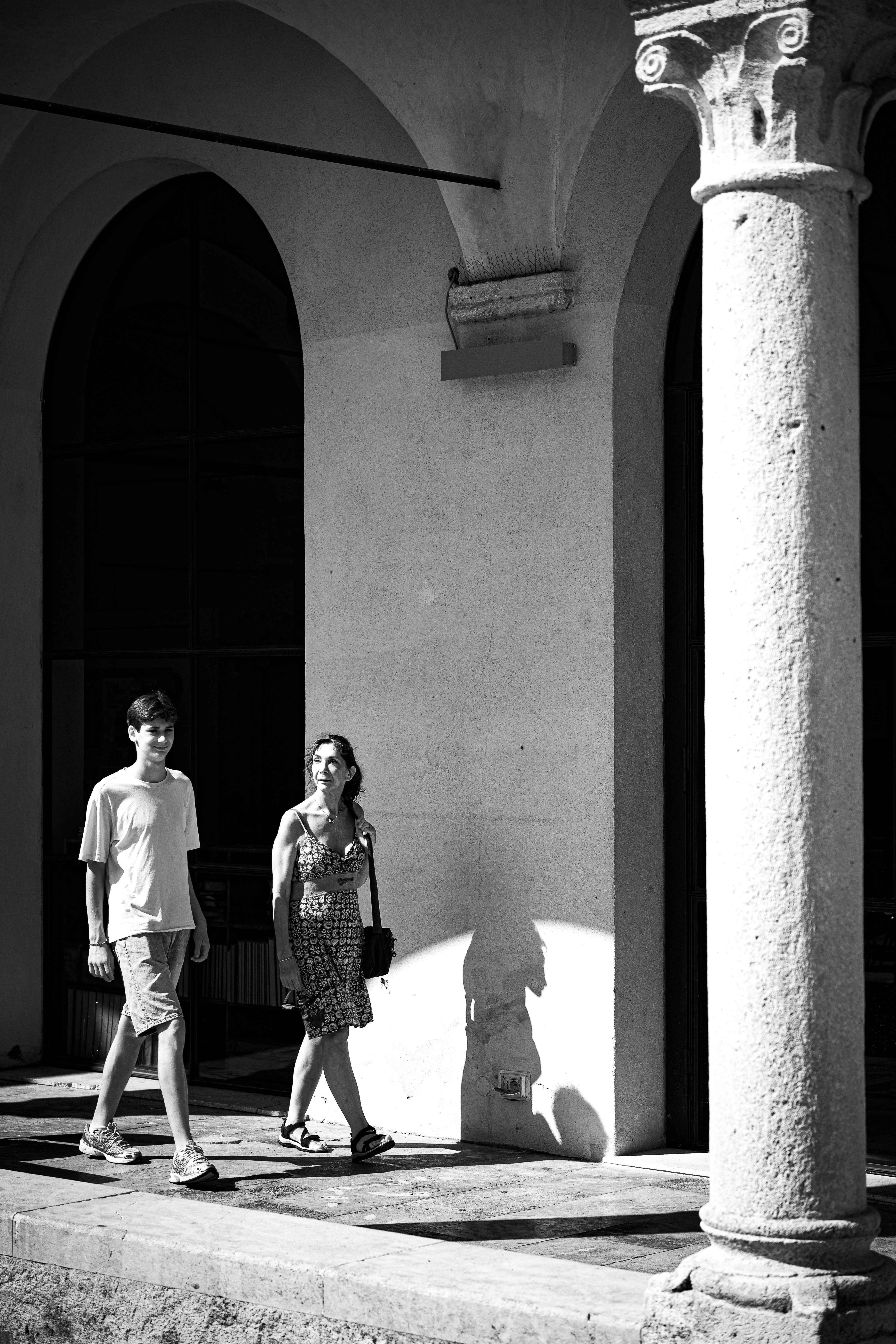 Shadowed Walk: Two Figures in a Sunlit Archway