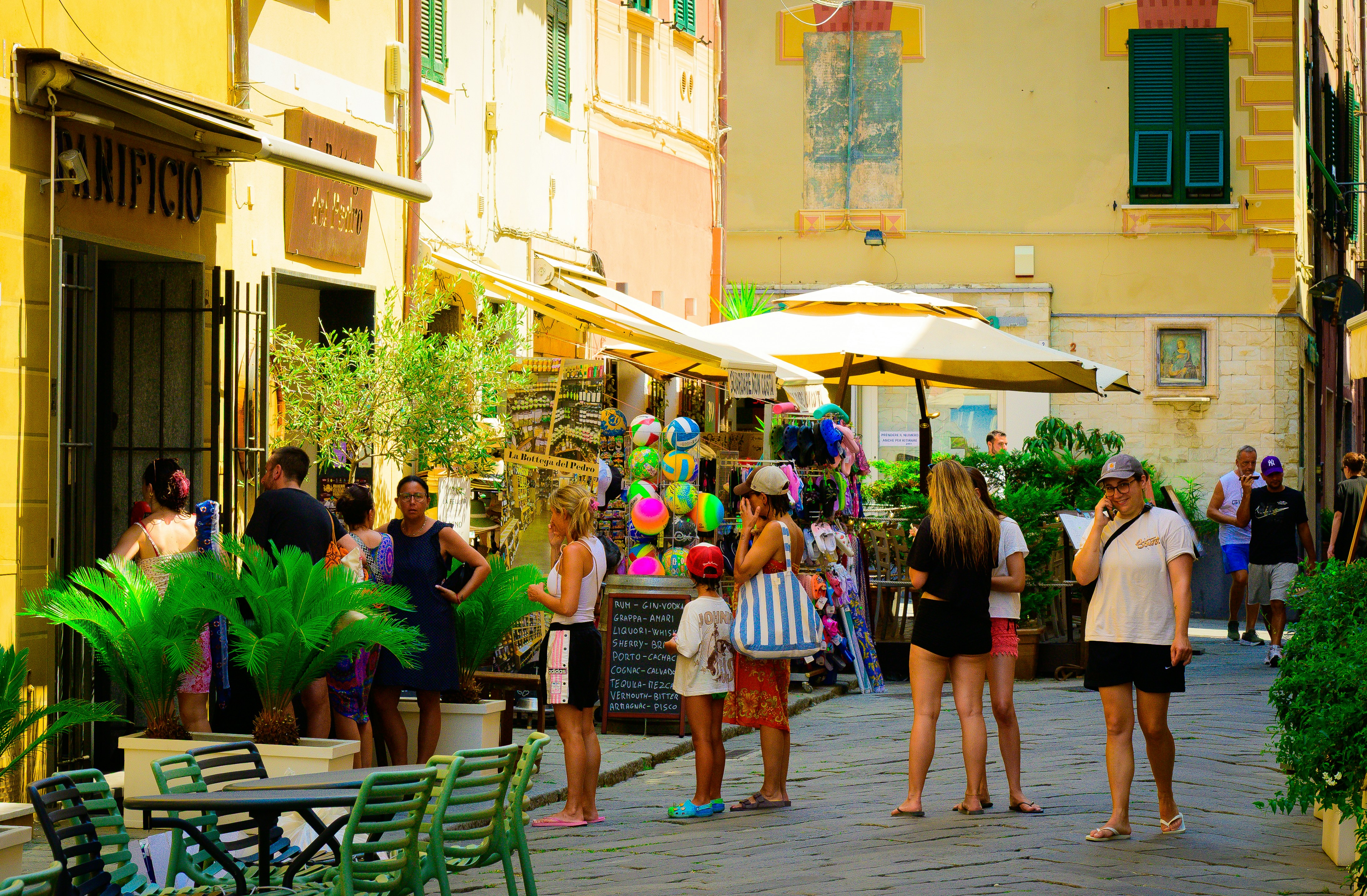 Sunlit street, colorful life: tourists, stalls, and green café corners