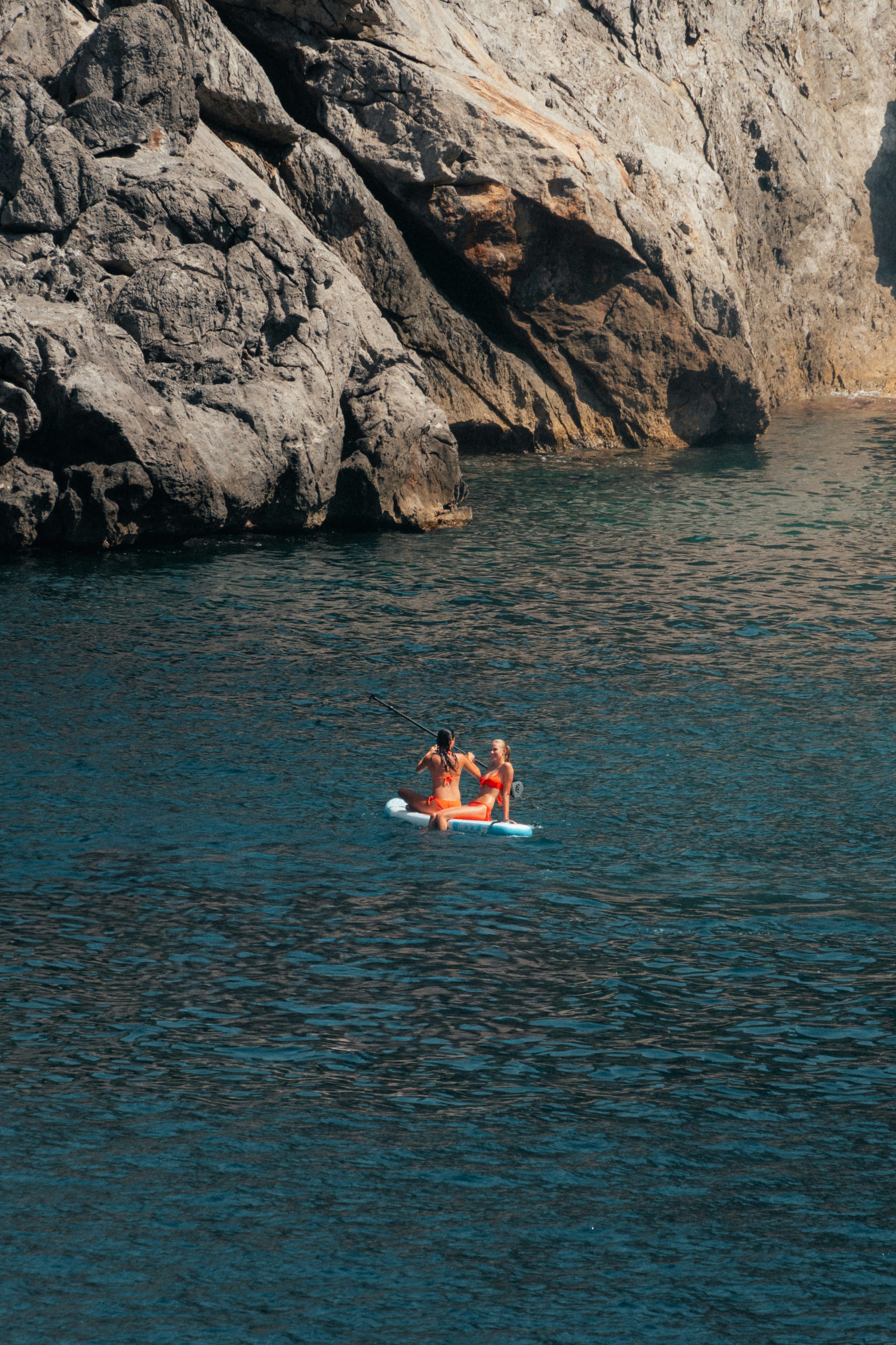 Two kayakers anchor in a turquoise cove beside rugged cliffs