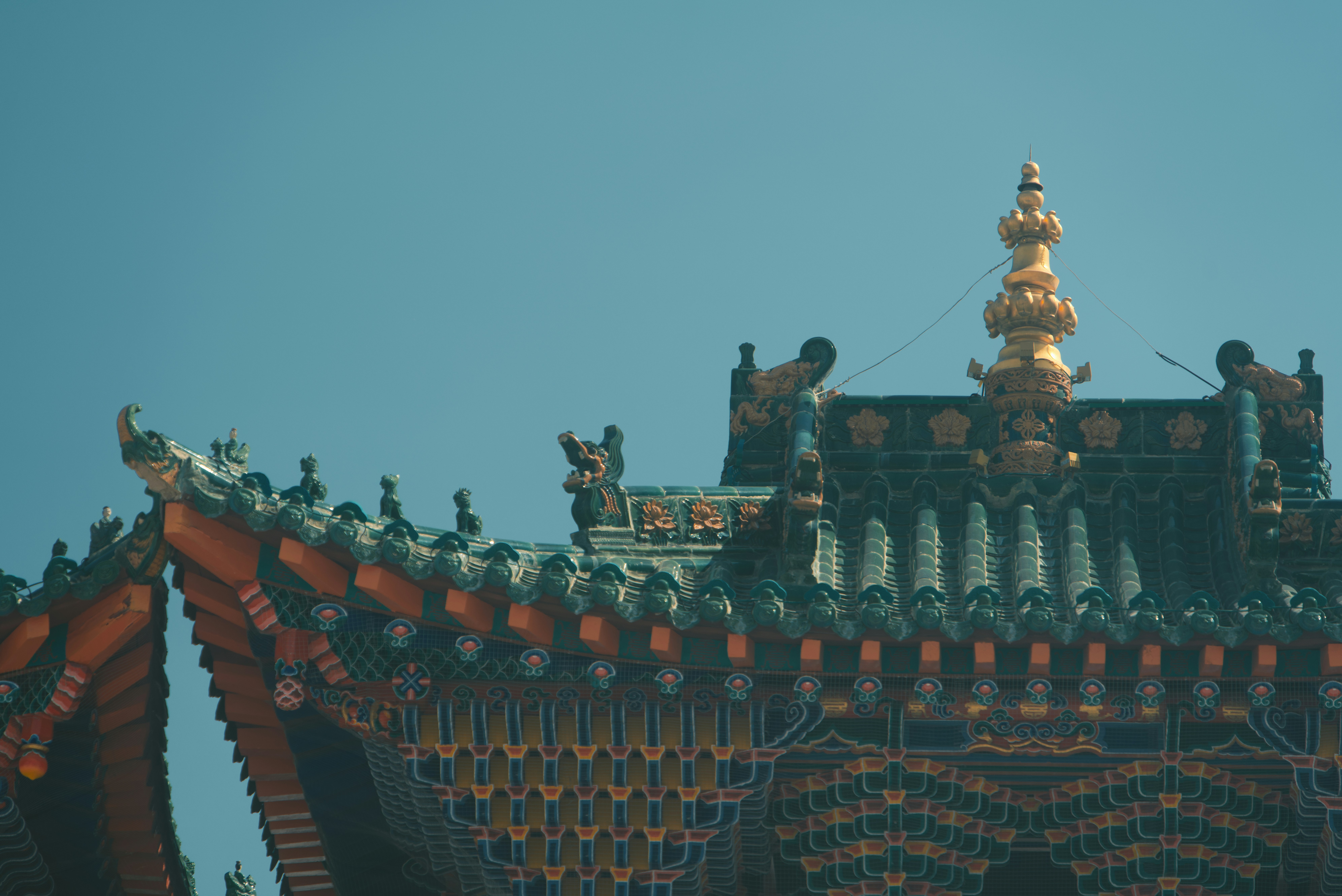 Ornate green tiled roof with gold finial against a clear blue sky