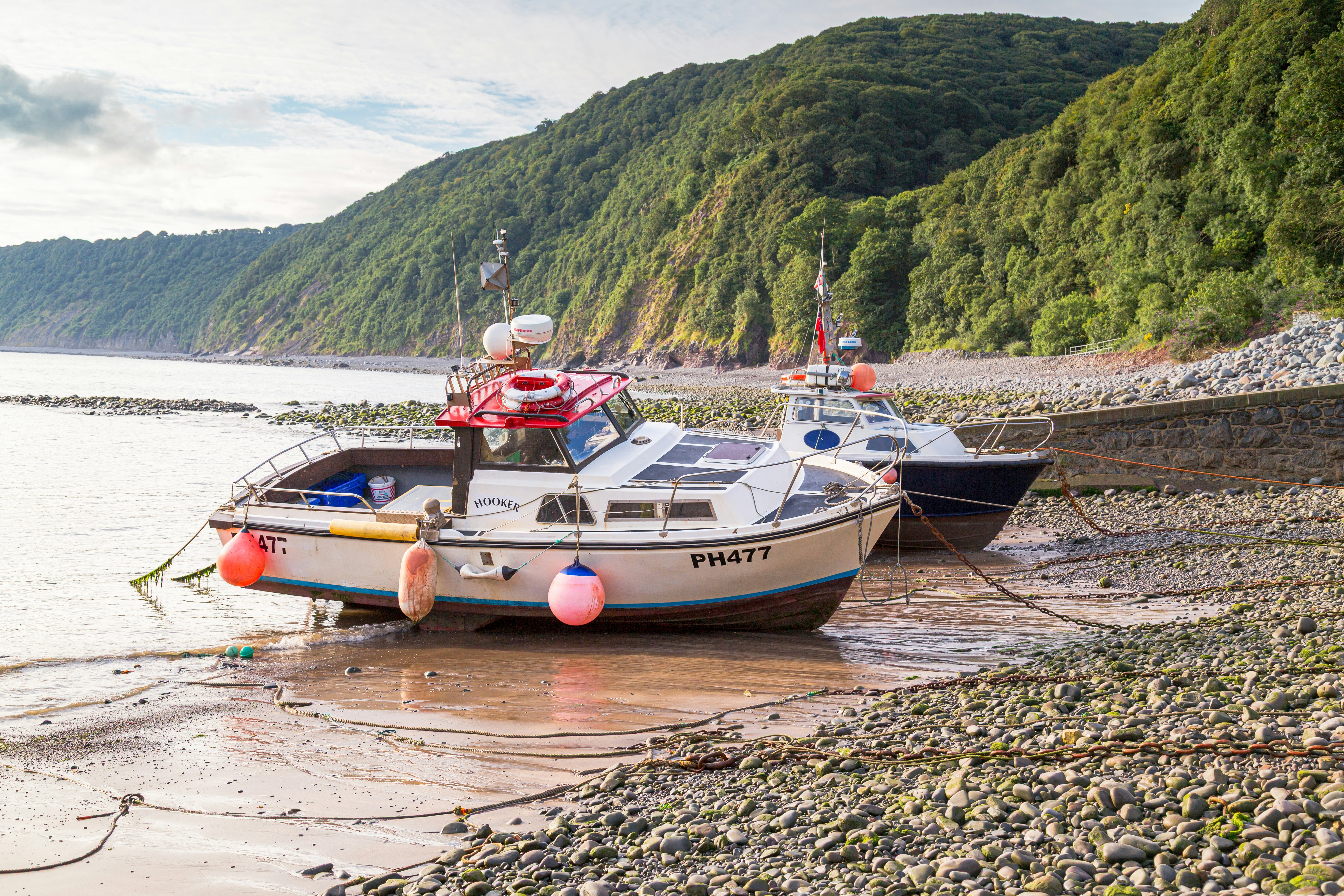 Boats Resting on a Pebble Shore Beneath Verdant Cliffs