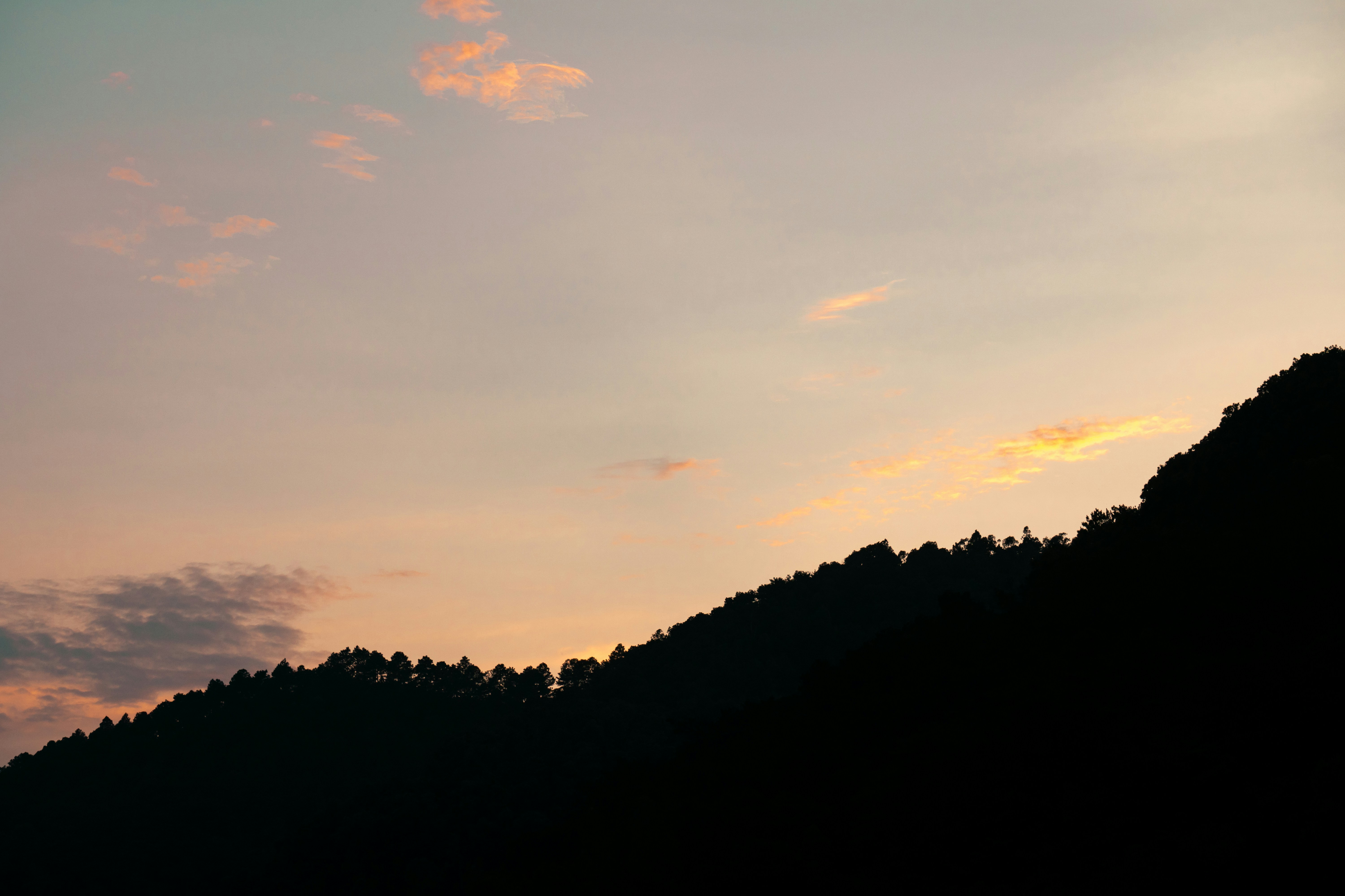 Soft sunset paints a quiet ridge in silhouette, with a gentle gradient sky and a darkened treeline. This scene emphasizes calm, natural contours and atmospheric light.