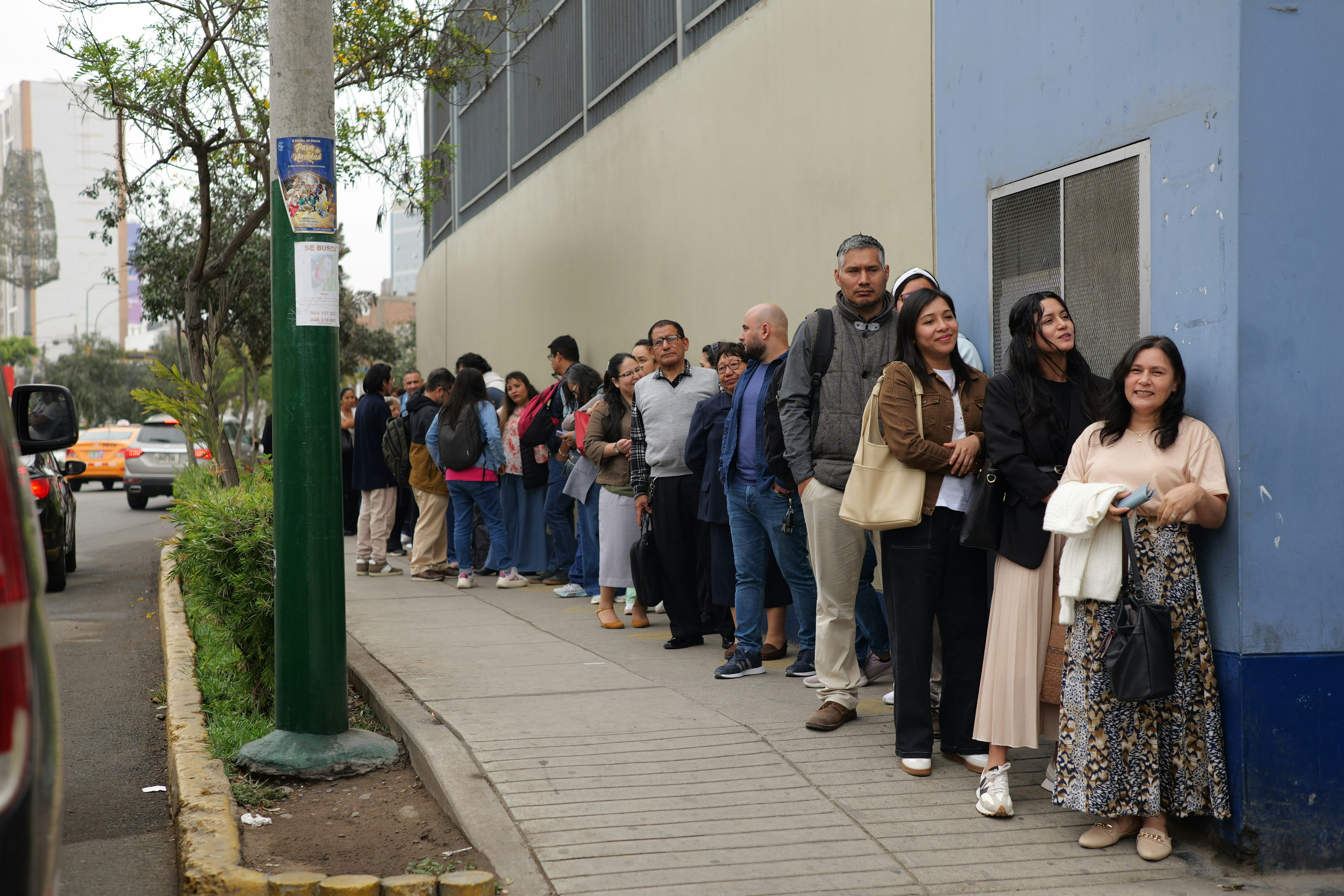 Queue Along a City Block: A Line of People Waiting by a Blue Wall