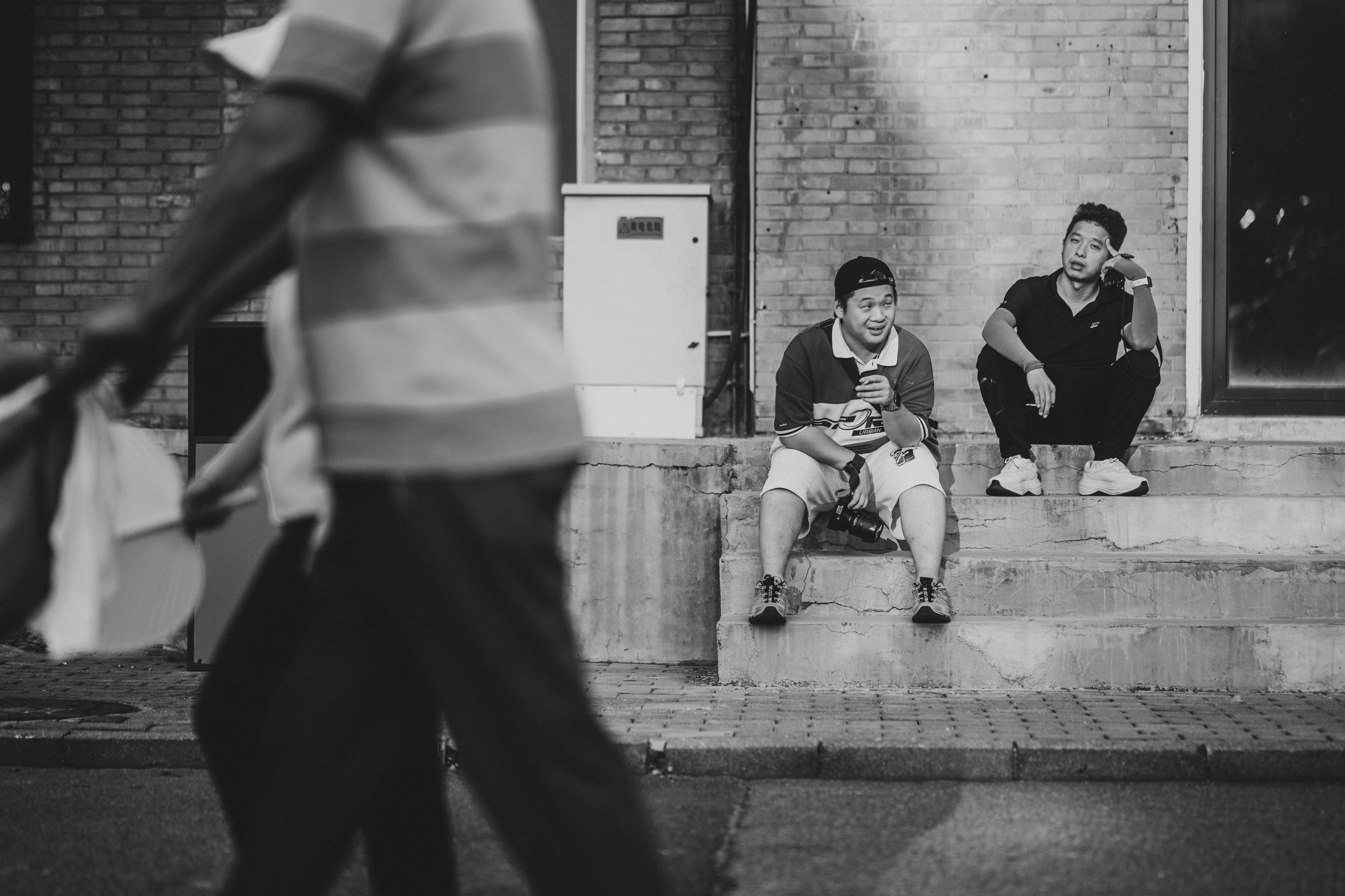 Two men sitting on concrete steps in front of a brick building