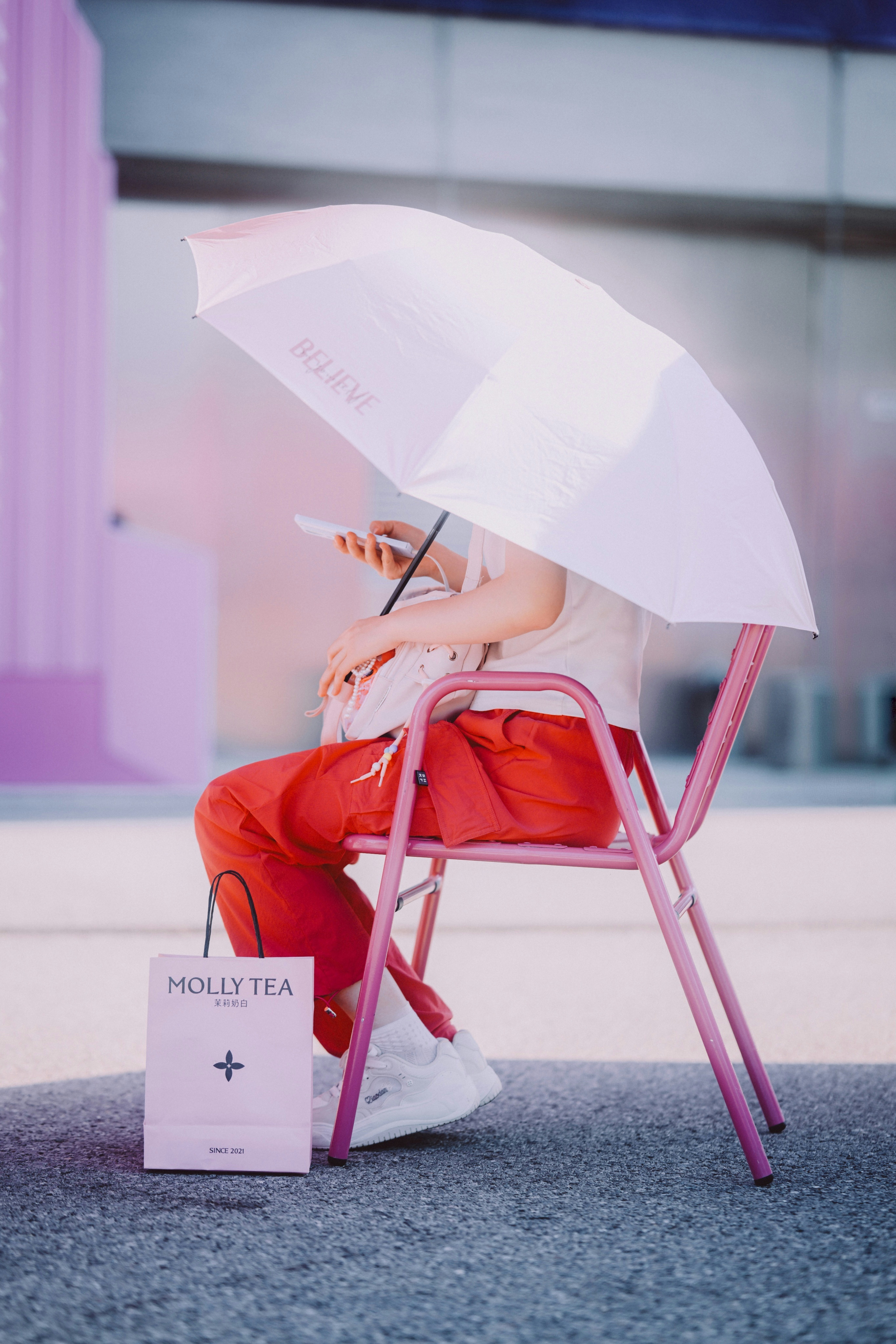 White Umbrella Over Quiet Focus: A Child Seated in Pink Chair with Gift Bag