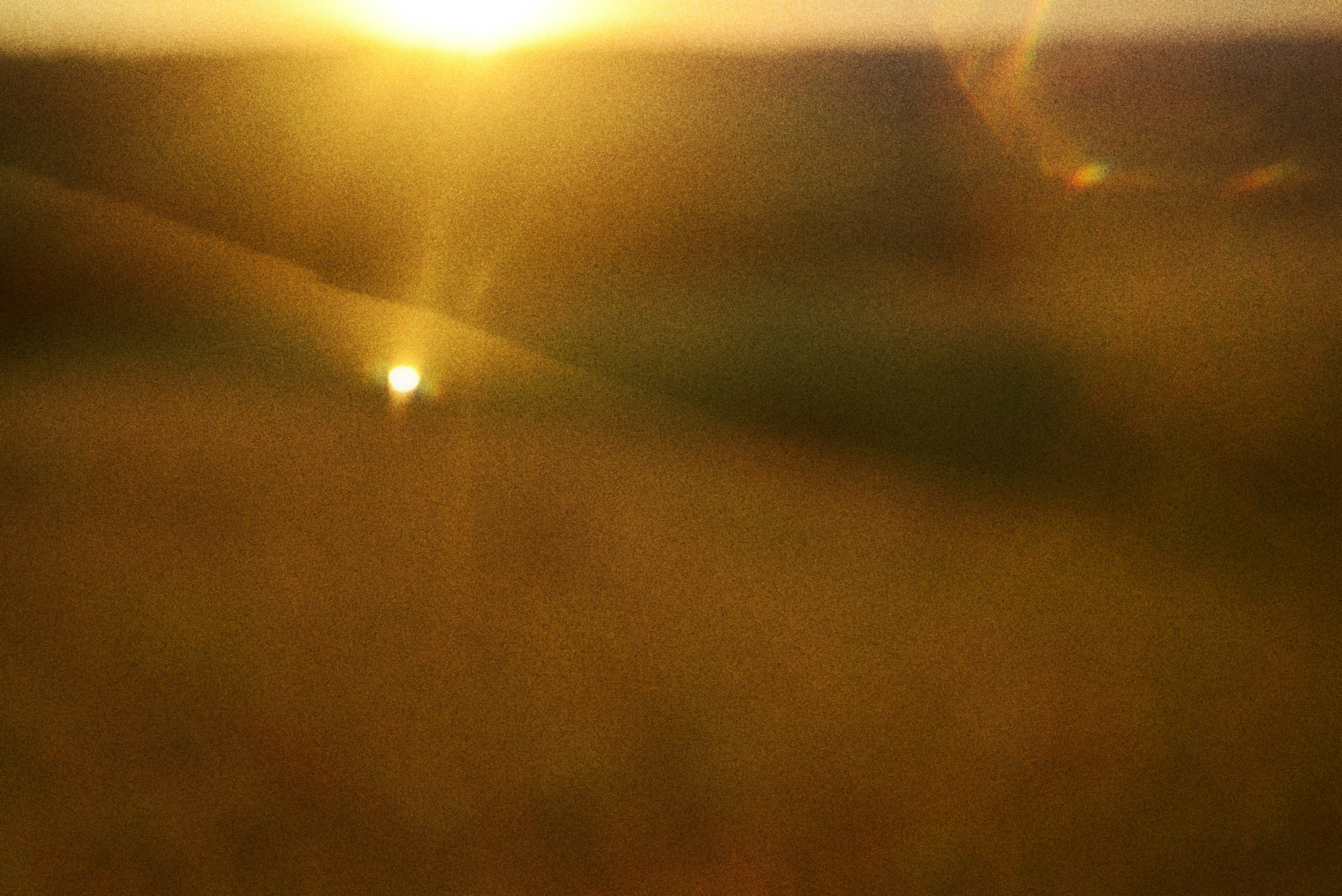 Soft, sunlit haze with a bright flare near the upper left, suggesting a distant horizon and warm atmospheric glow.
