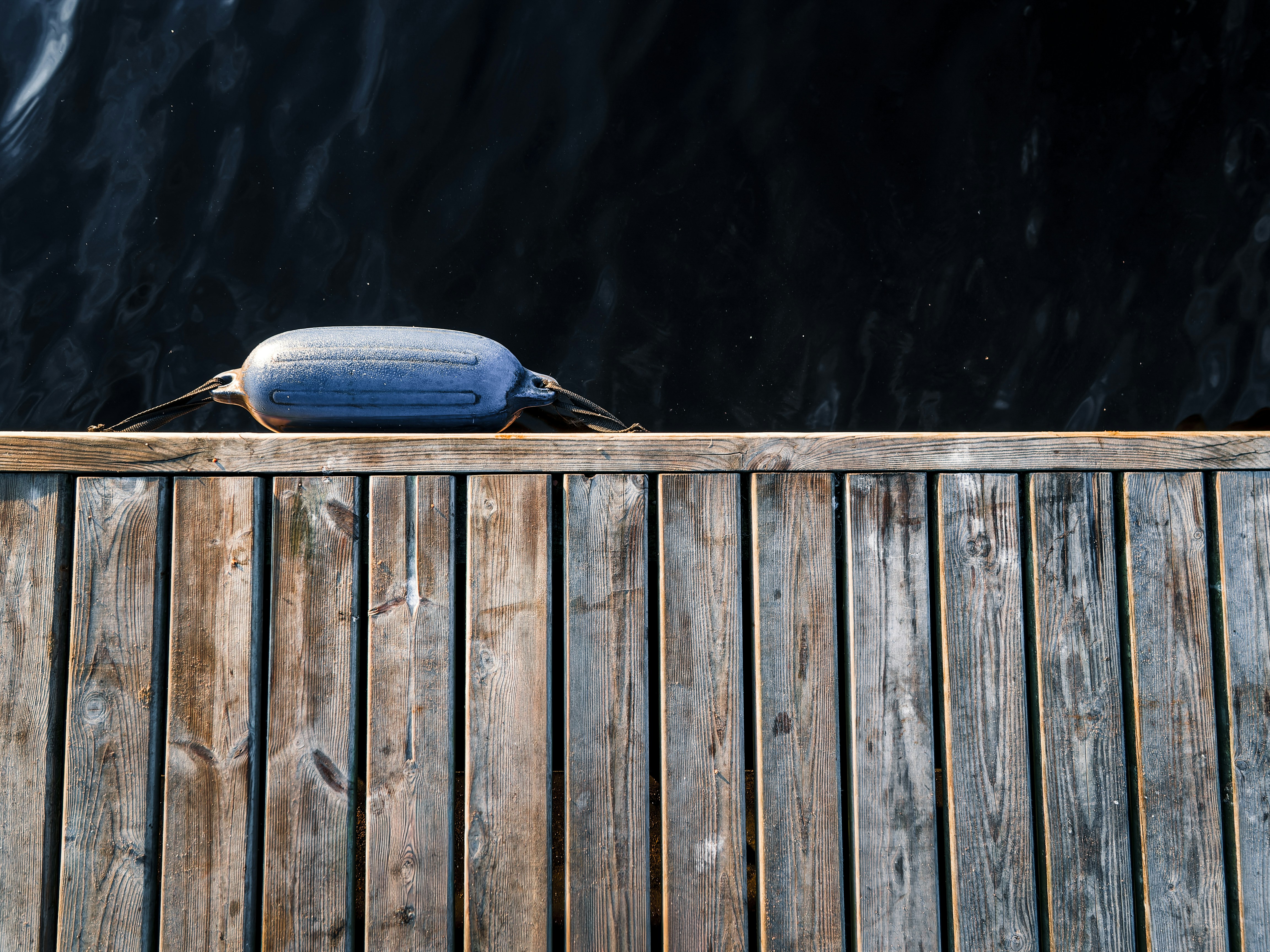 A solitary buoy resting along weathered planks at water’s edge