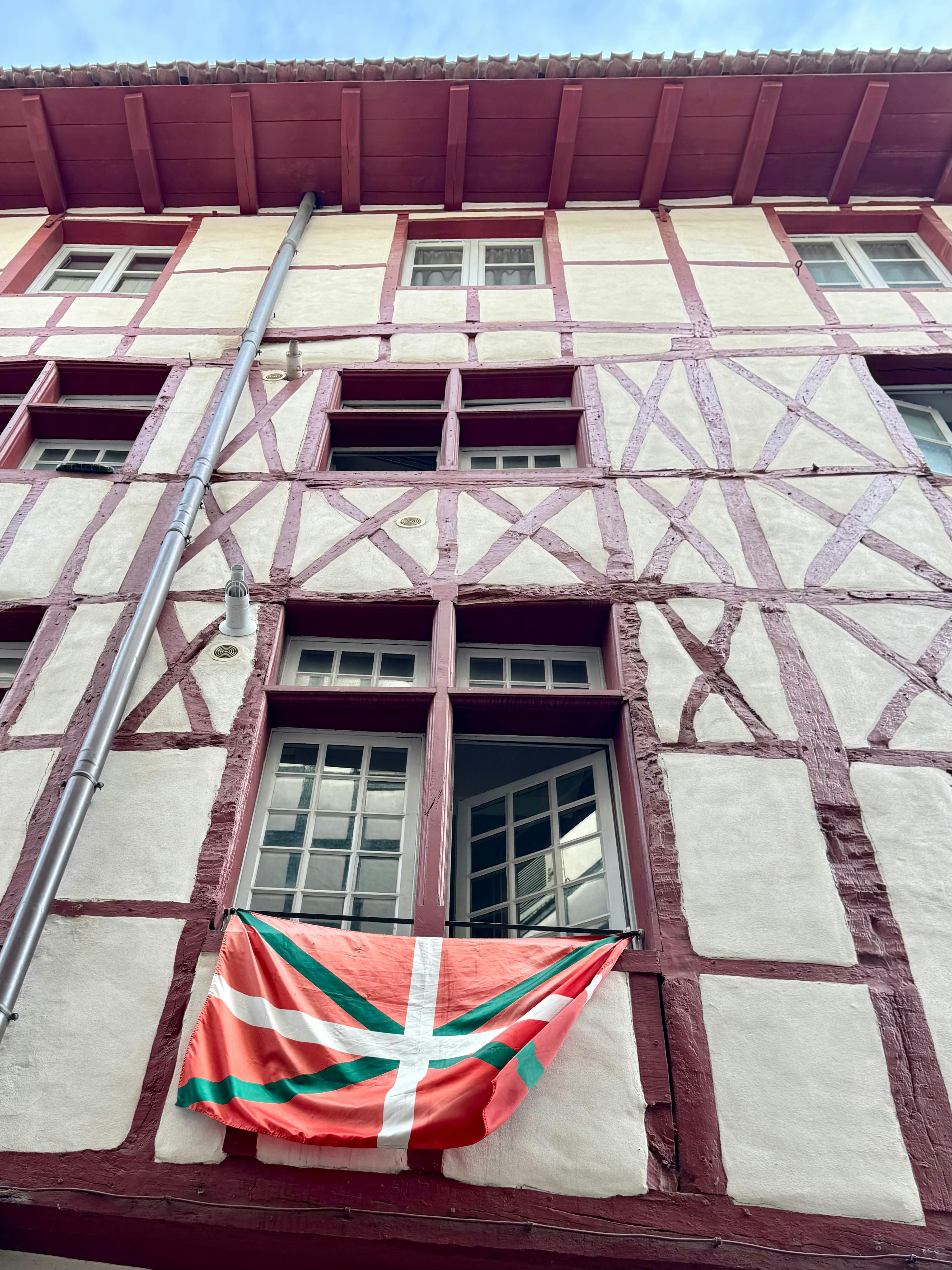 Flag hanging from a timber-framed European building with pink-brown beams and white infill, windows above, captured in daylight.