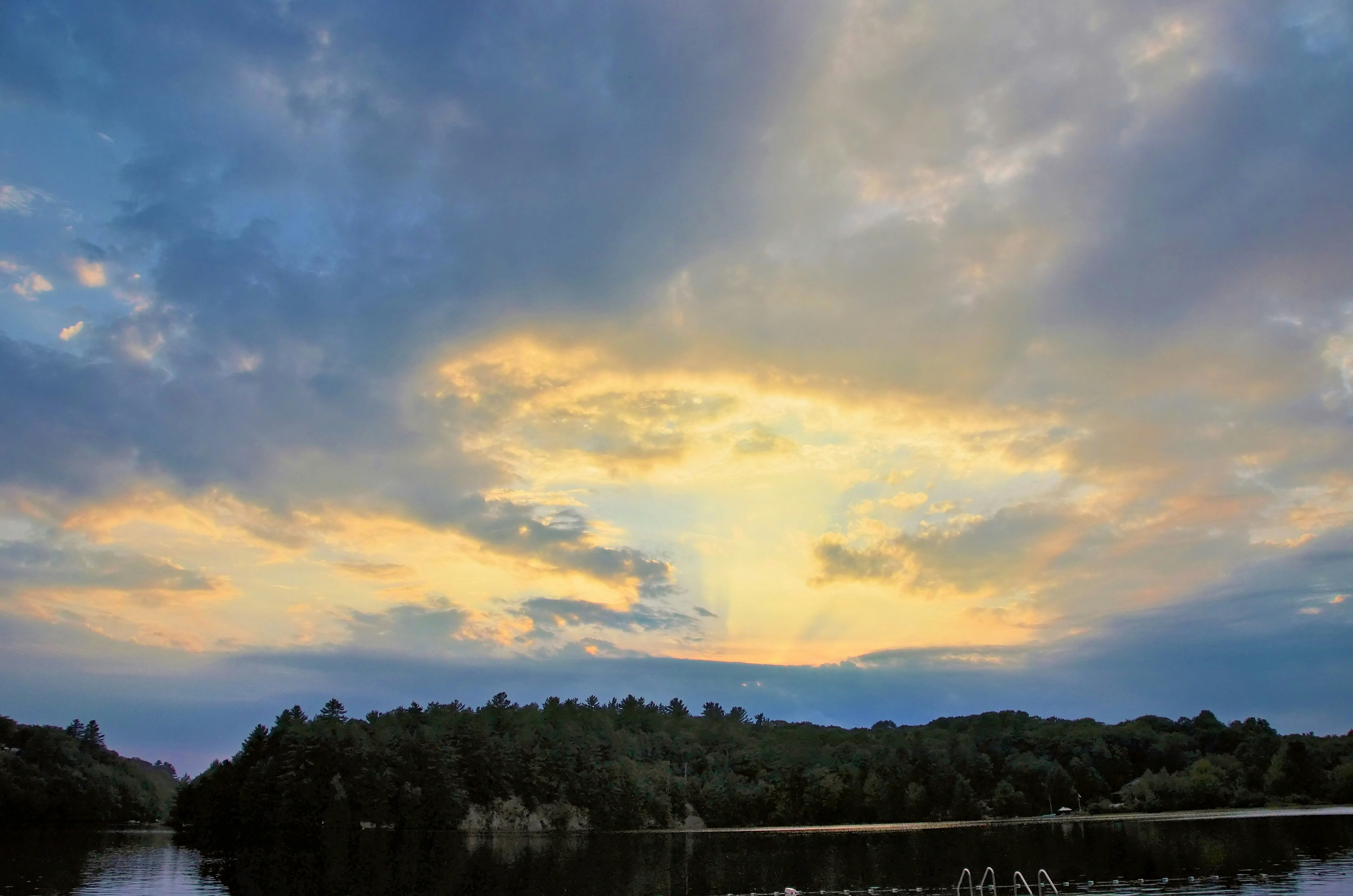 Sunlit gap over tranquil lake reveals a quiet forest horizon