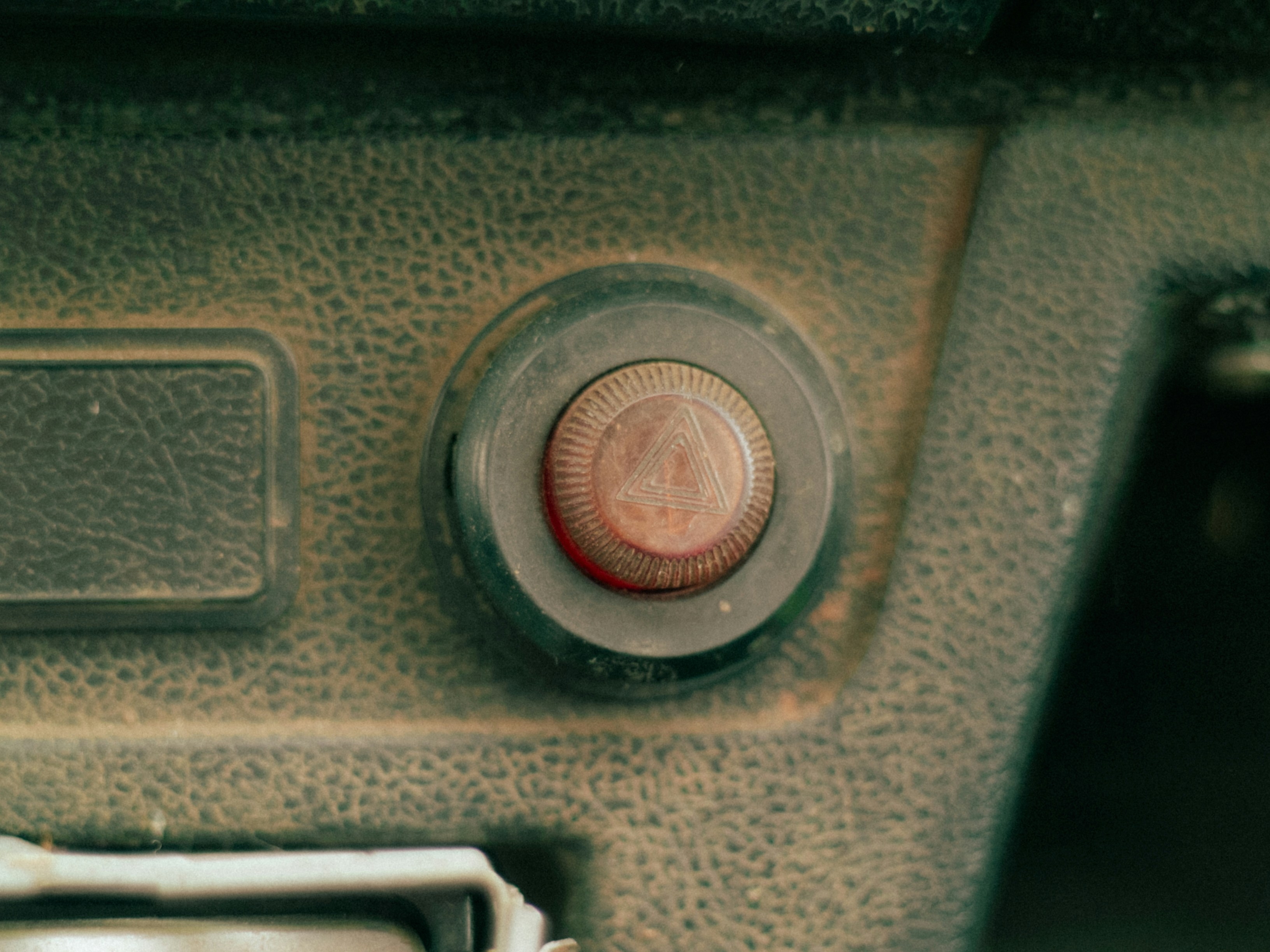 Close-up of a textured vintage car dashboard knob with surrounding rugged plastic; emphasizes tactile detail and weathered surface.