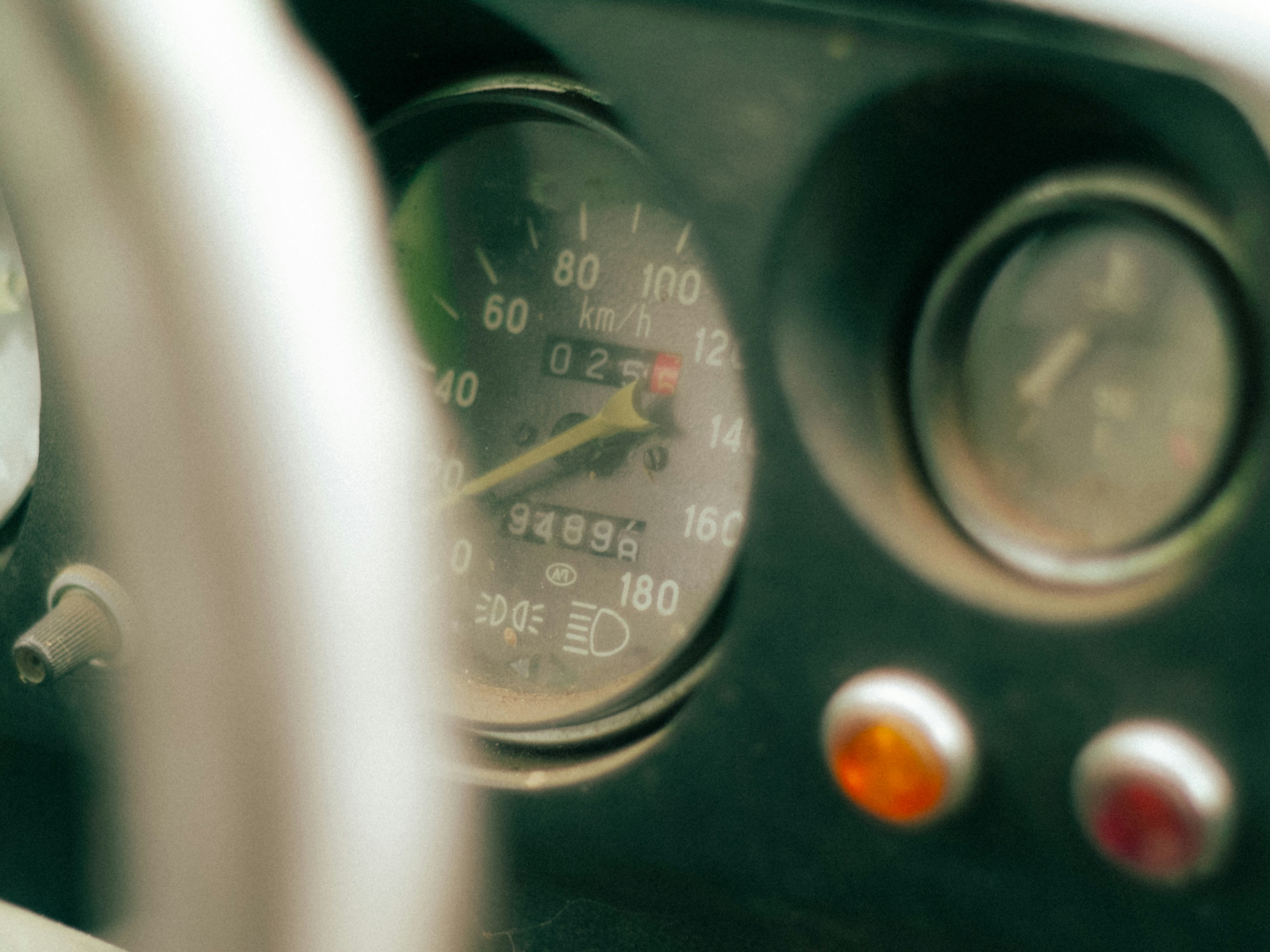 Close-up of a vintage car dashboard with a speedometer and blurred gauge cluster, emphasizing tactile controls and aged materials.