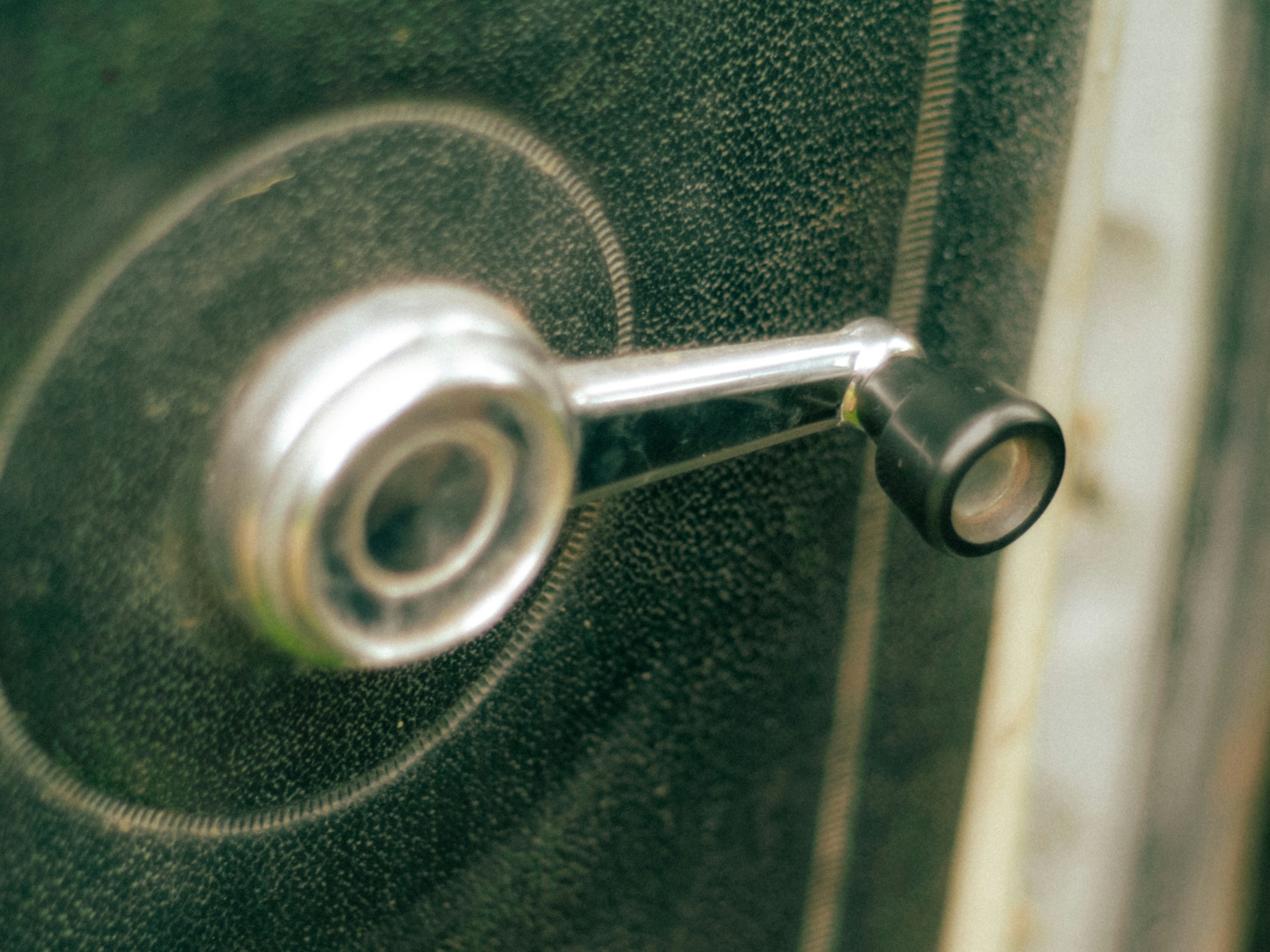 Close-up of a metal door knob and lever set against a textured, dusty green panel, highlighting patina and hardware detail.