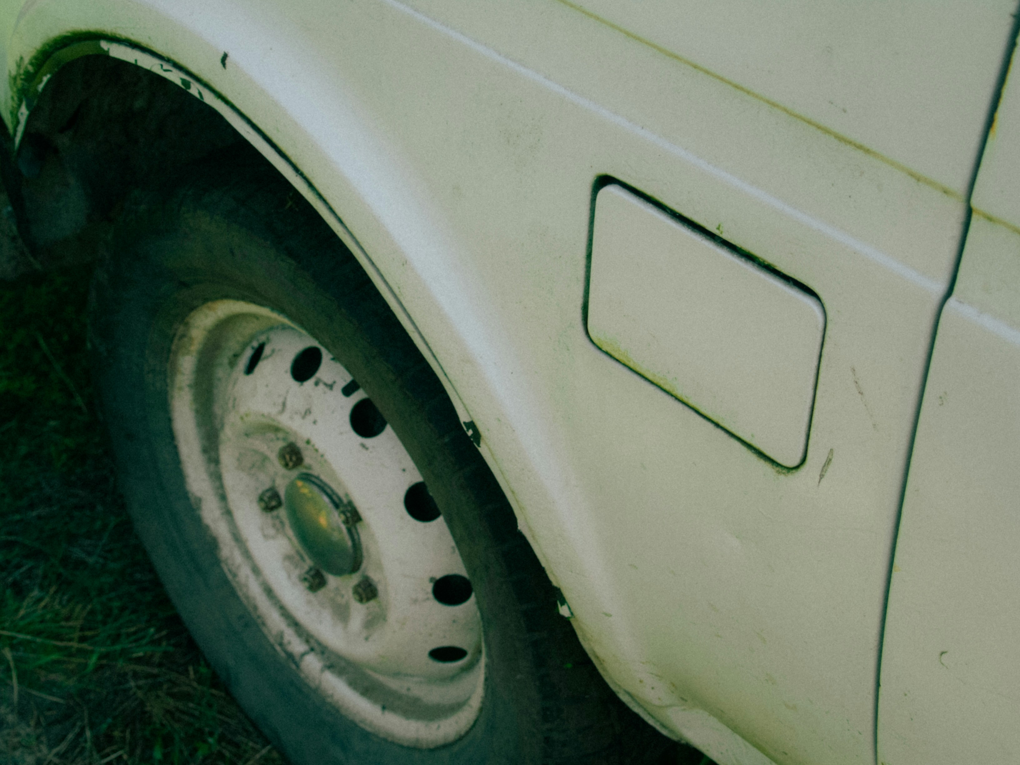 Close-up of a pale vehicle fender and wheel well with a dusty steel rim. A practical, utilitarian view highlighting the aging exterior and the wheel hub area.