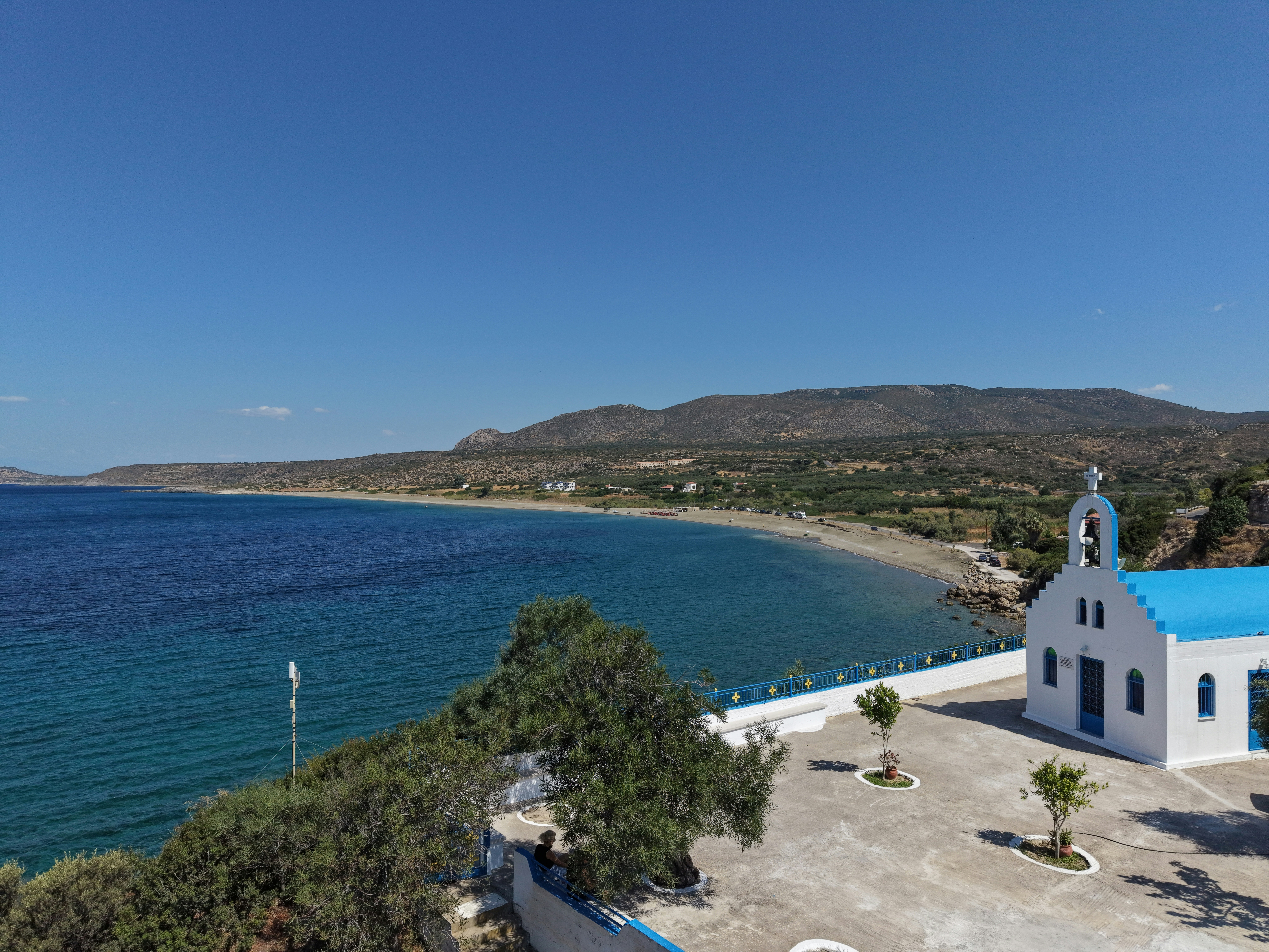 Blue-roofed chapel by the Aegean shore under a clear afternoon