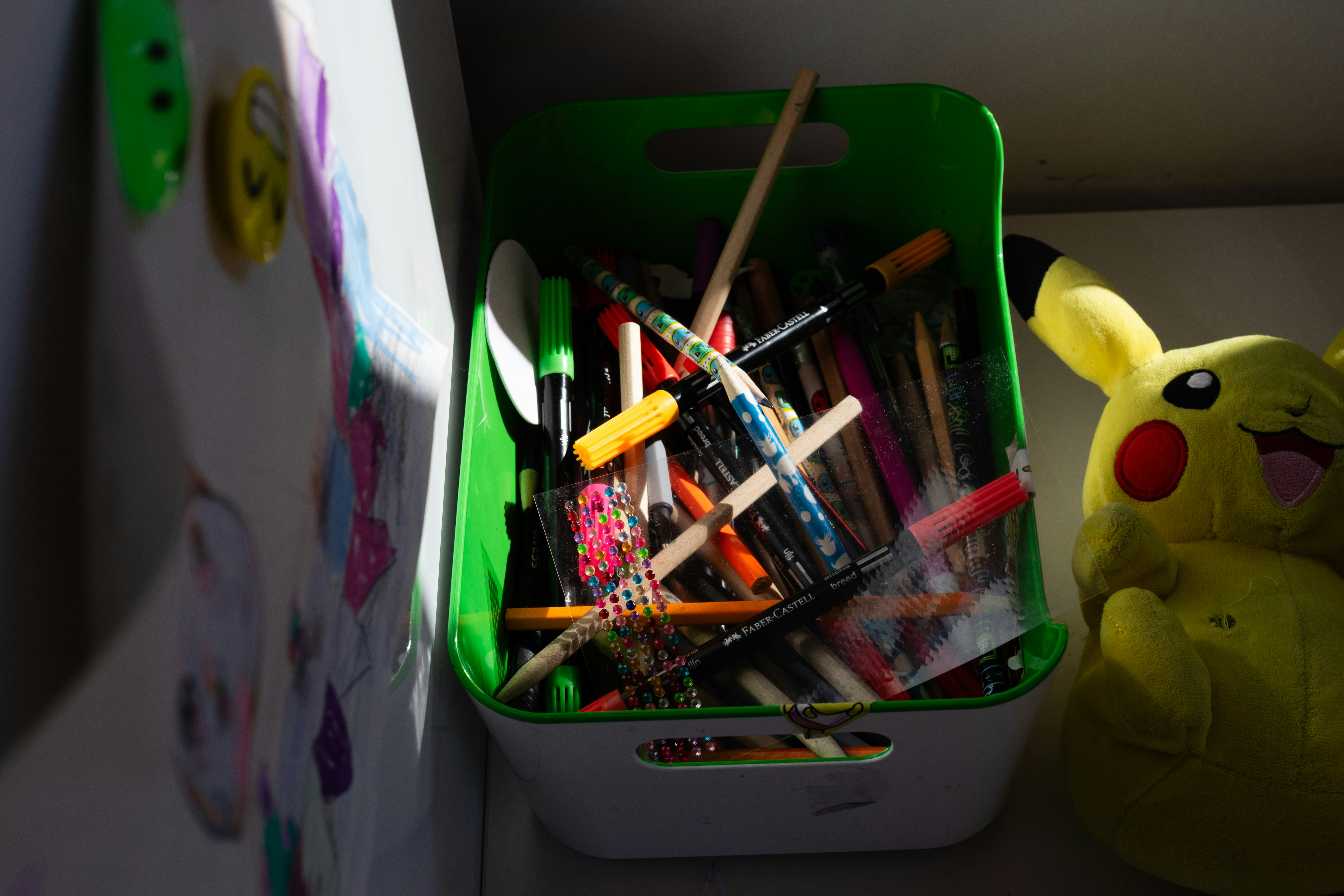 A green and white plastic bin filled with assorted markers and pencils