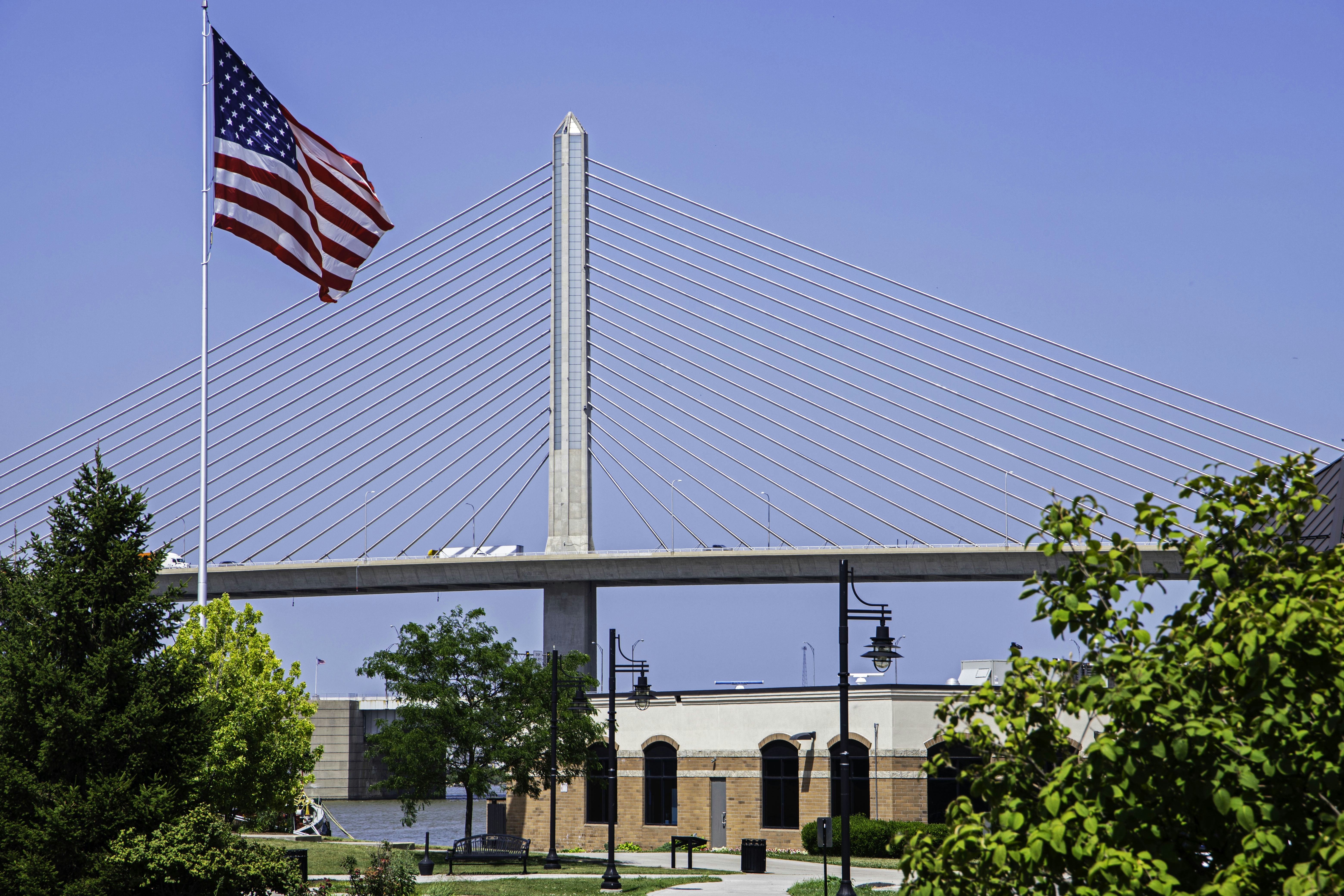 The American flag flying near a cable-stayed bridge over a river