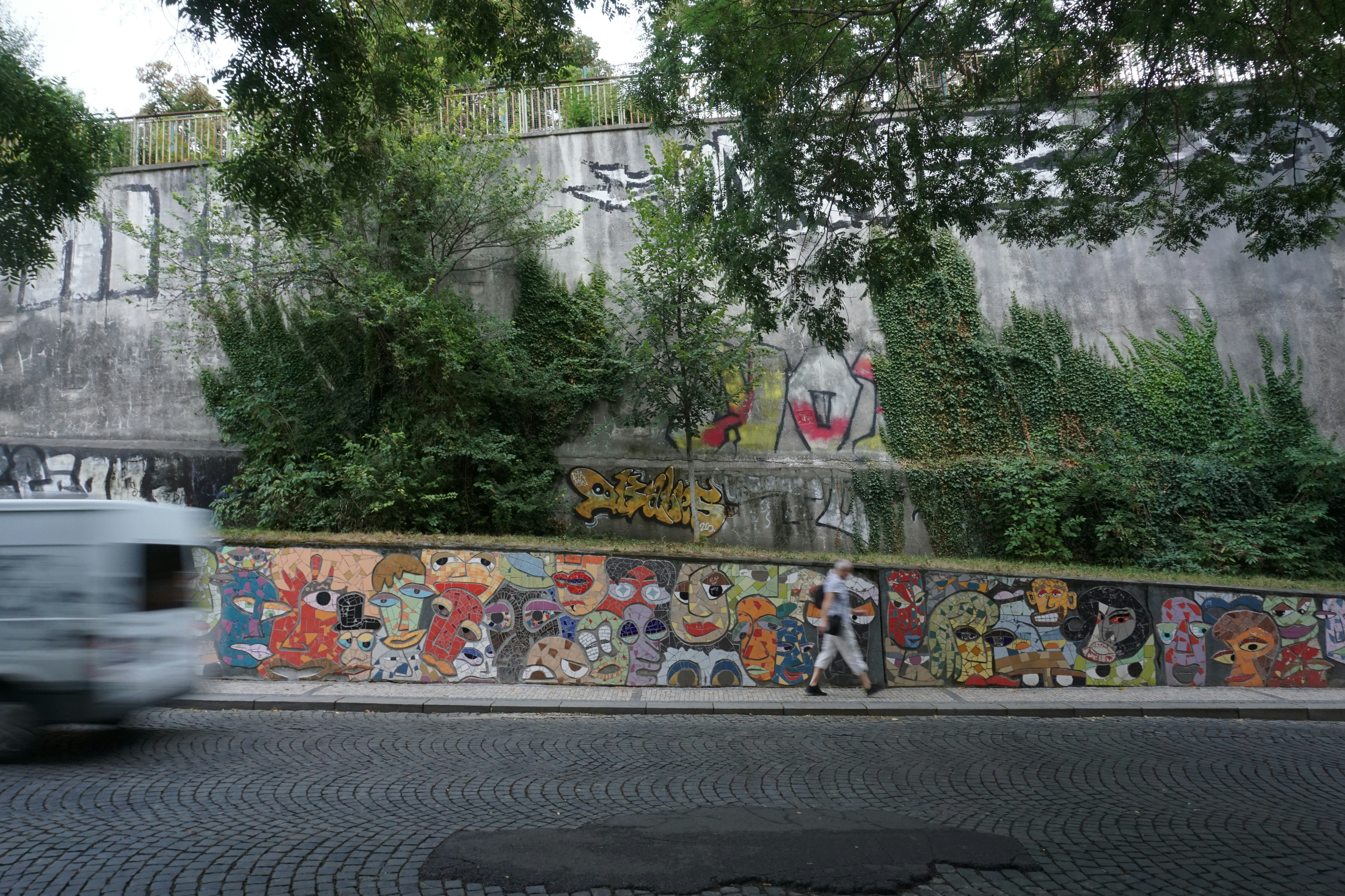 A person walking past a colorful mosaic wall on a cobblestone street
