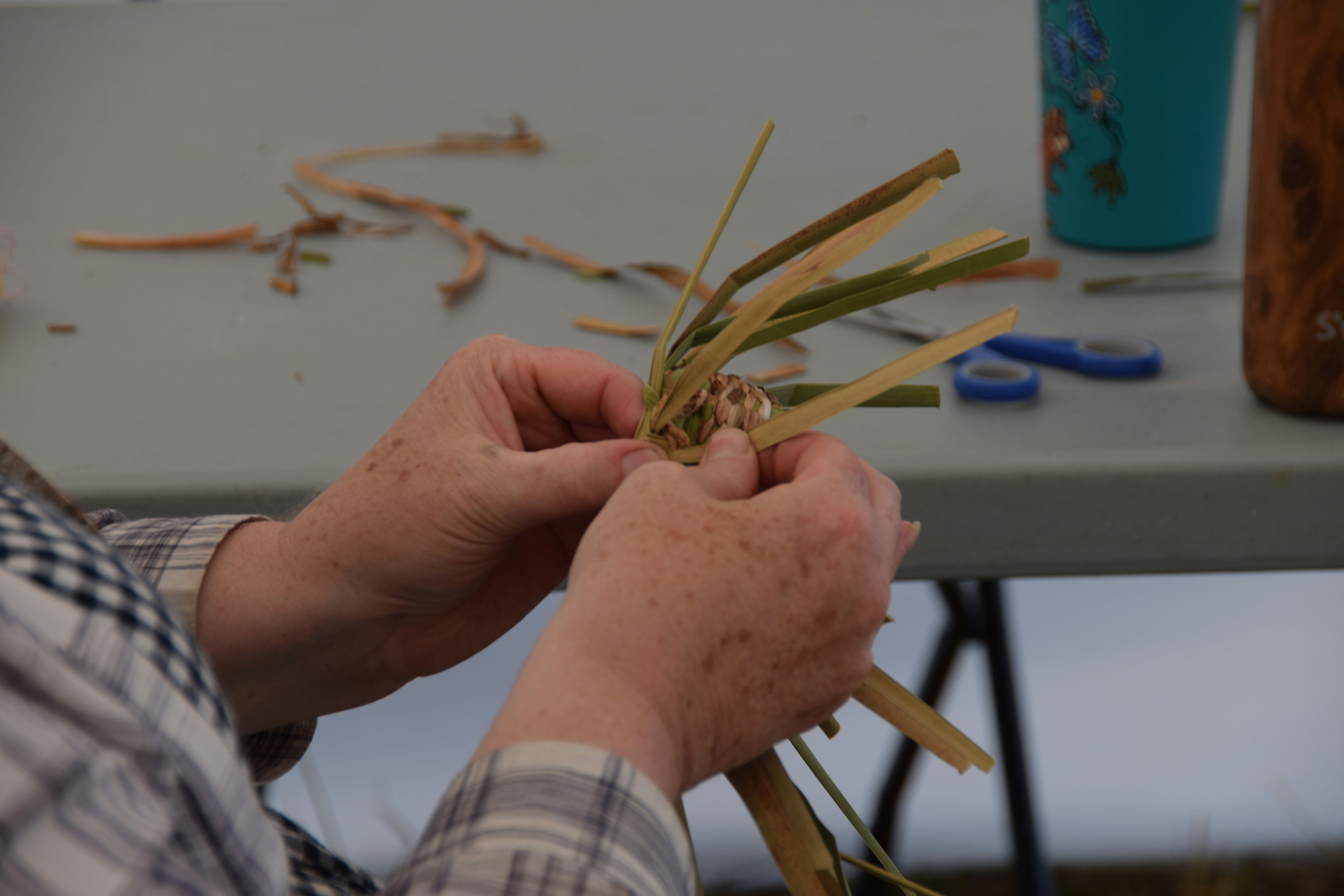 Hands weaving a plant crown from yard scraps on a worktable