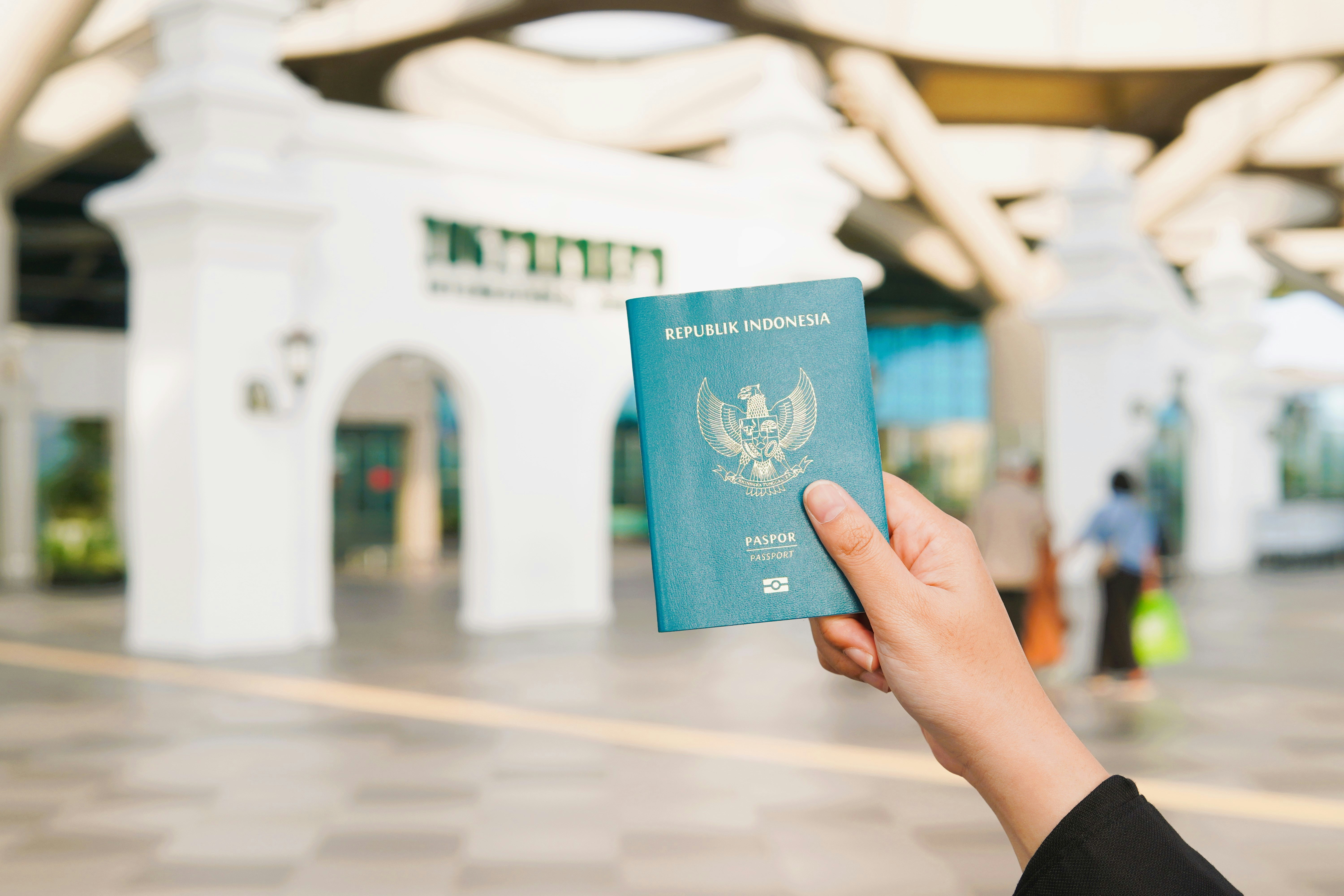 Hand presenting a turquoise passport in a bright public space
