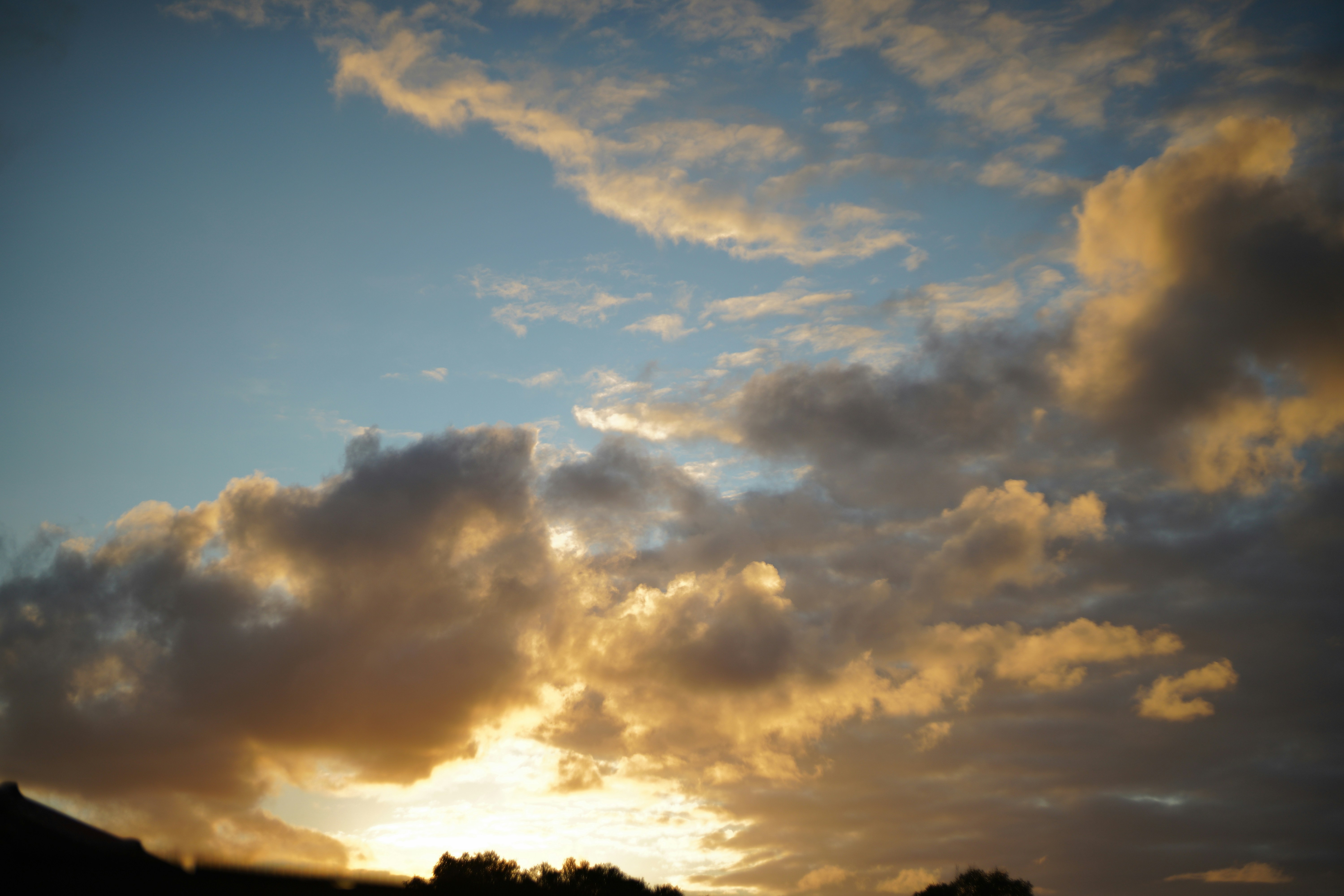 Vibrant sunset sky over a silhouetted ridge with dramatic clouds and warm golden light.