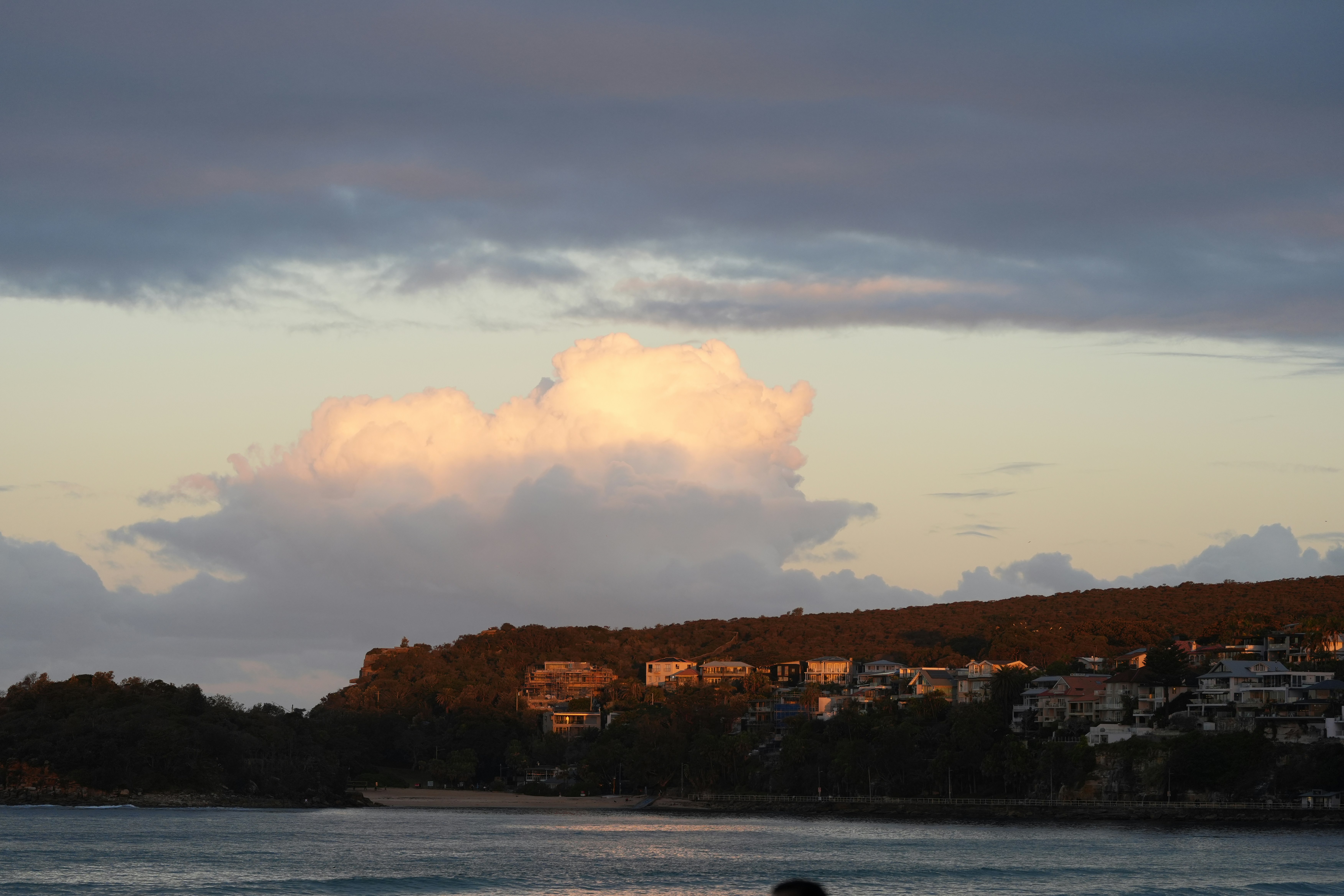 Golden Hour Coastline: Distant houses and calm sea under a puffy sunset cloud