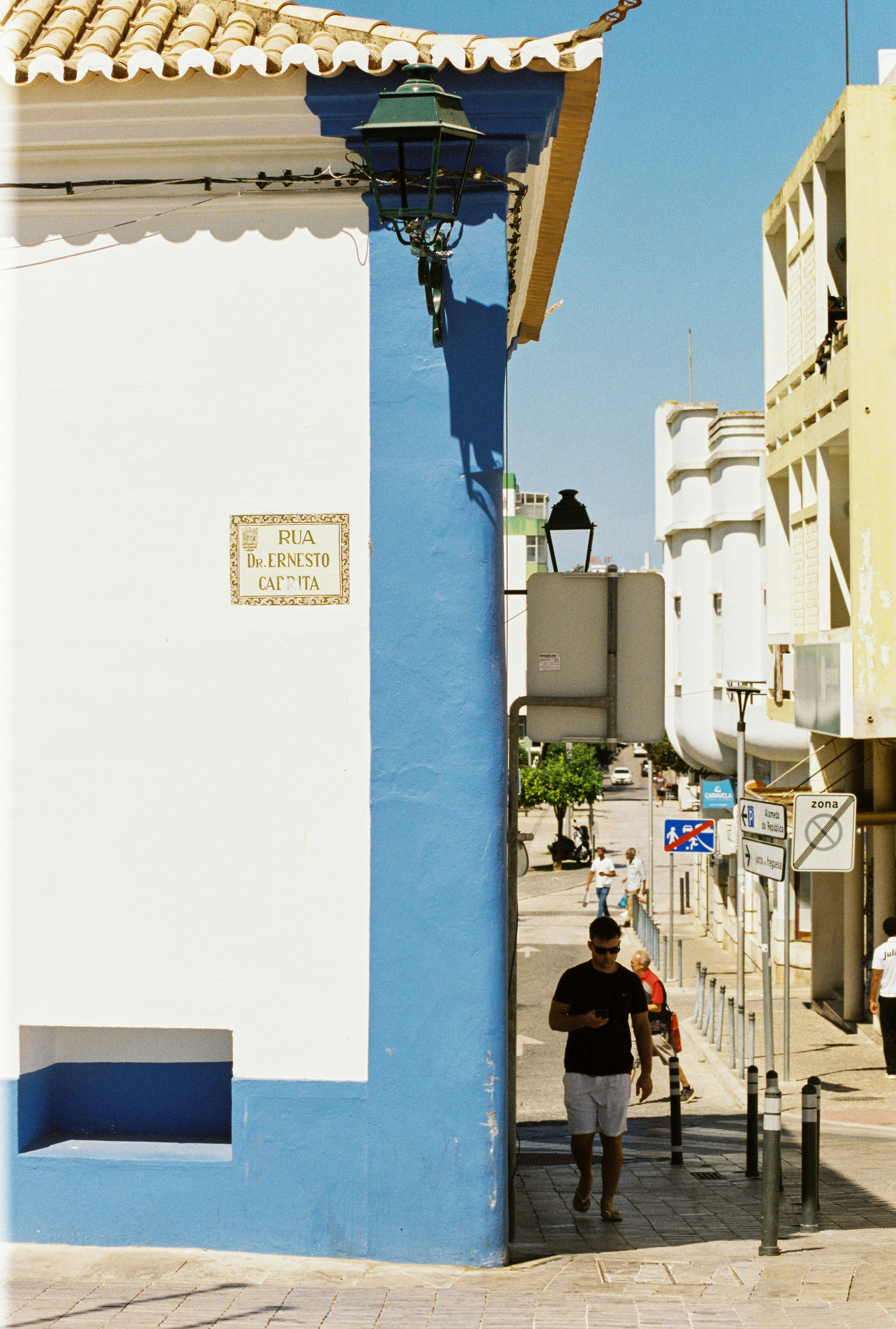 Blue-walled street corner with shadowed lantern and strolling figures