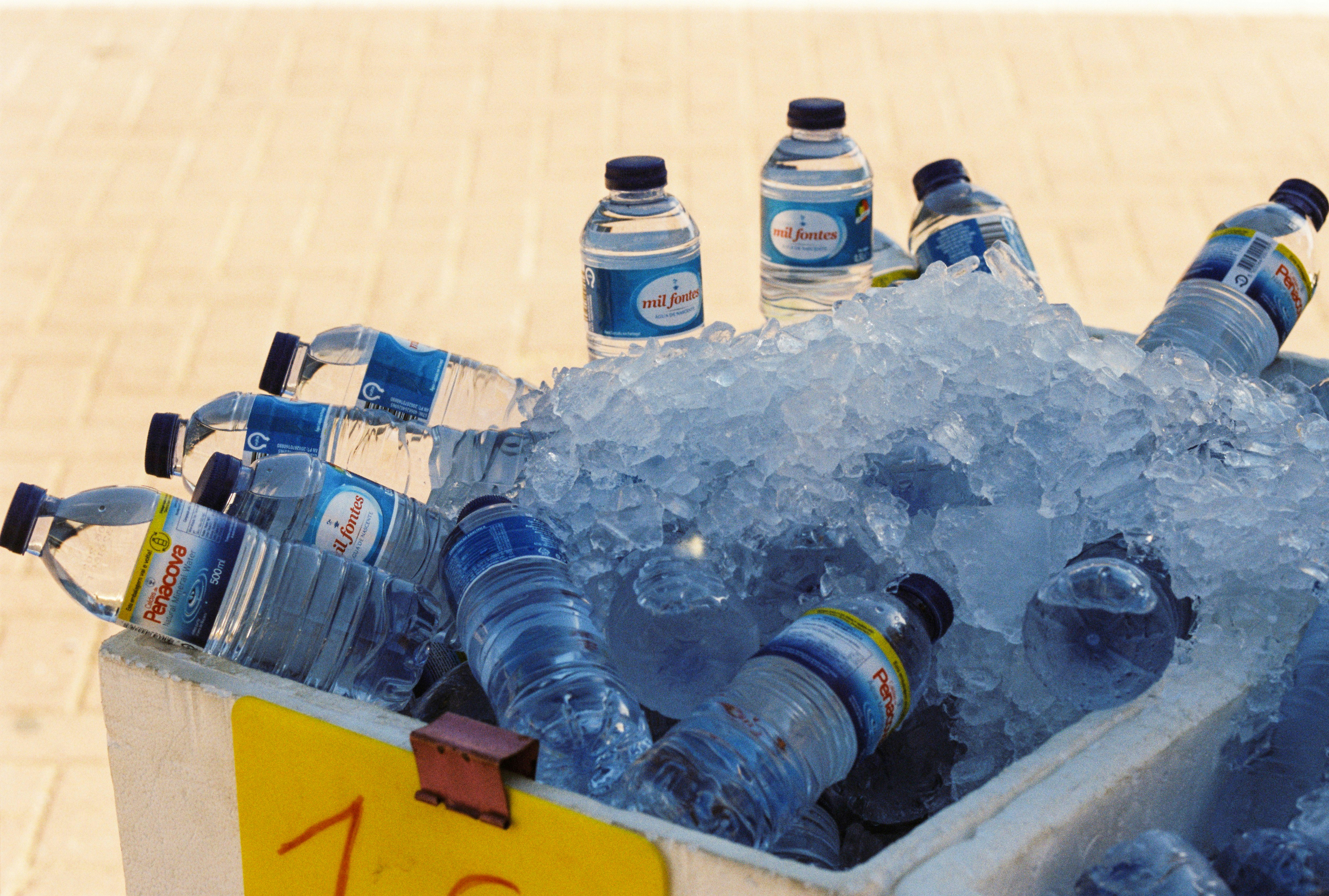 Bottled water chilling in a foam cooler filled with crushed ice, outdoors on a sunny day.