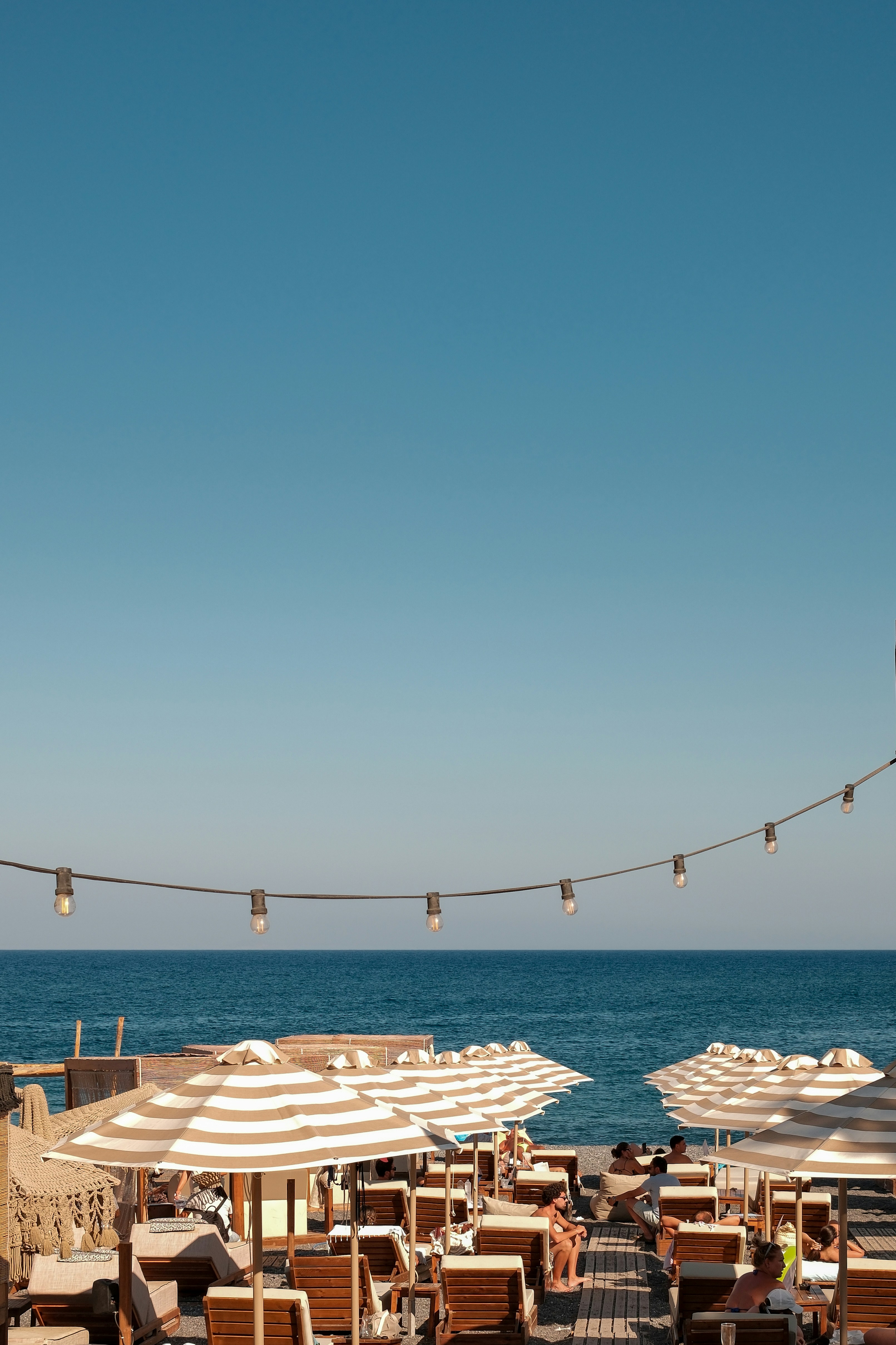 Row of striped umbrellas and lounge chairs along a sunlit seaside deck