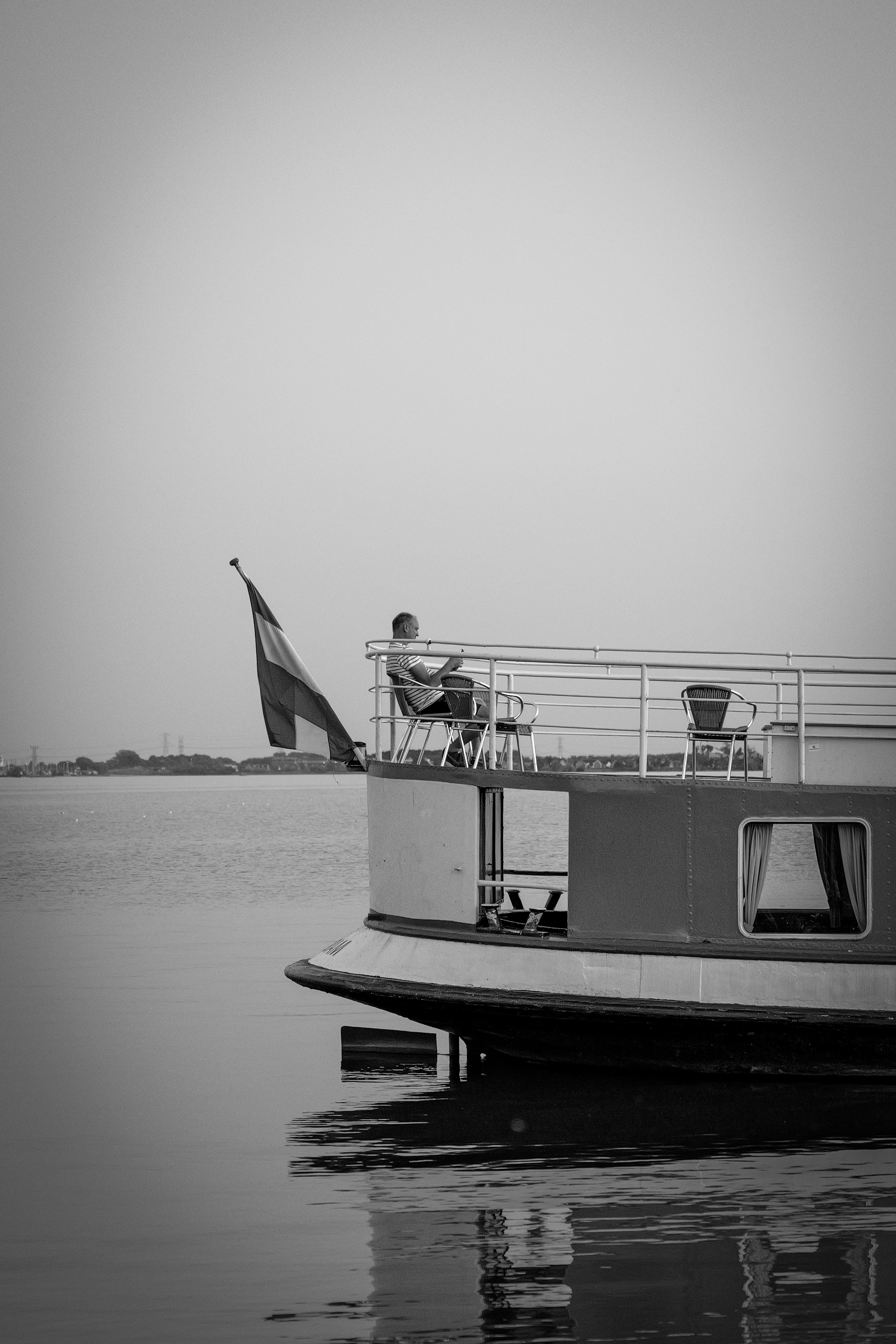 A person in a striped shirt on the deck of a boat with a flag