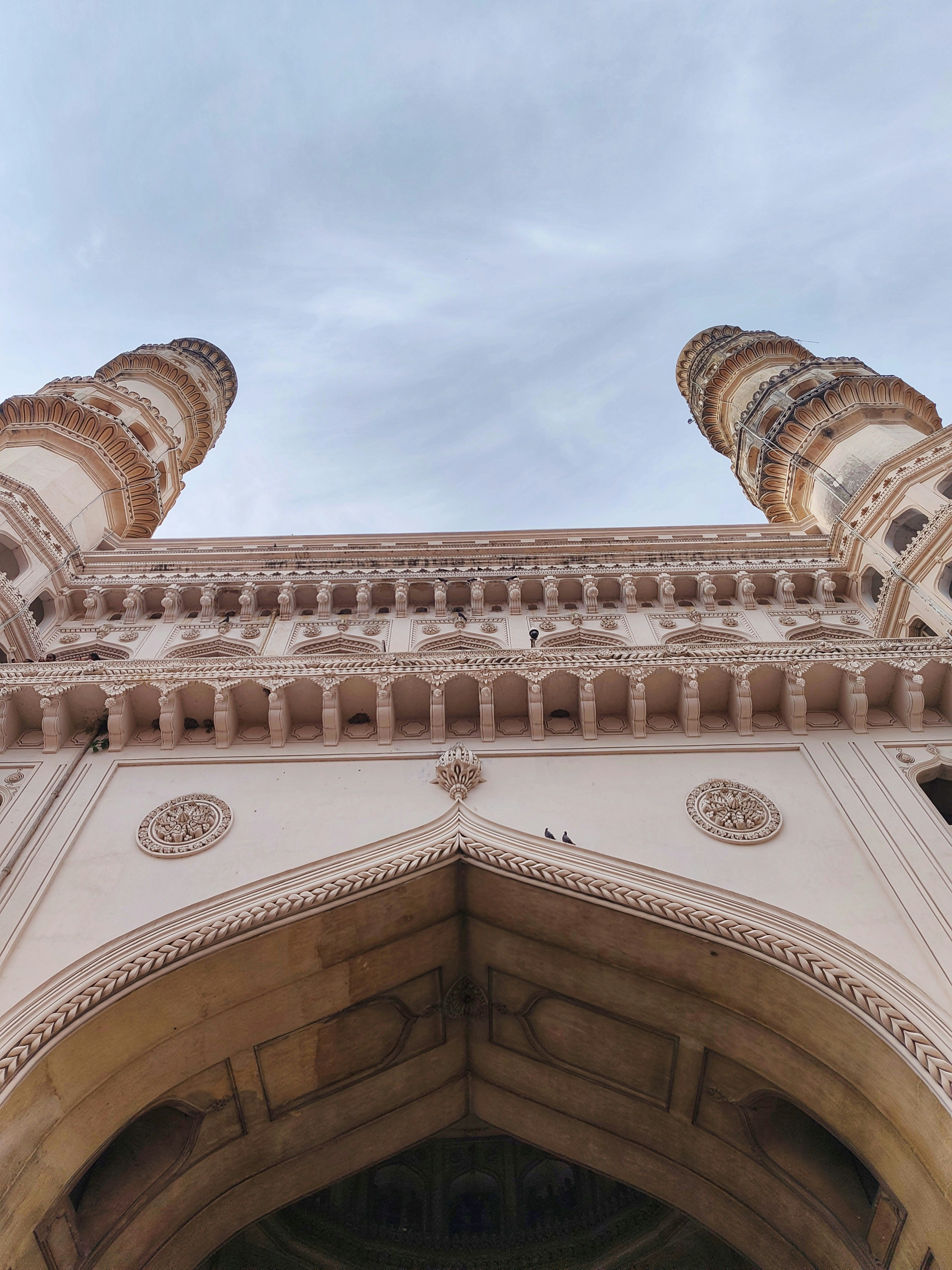 Intricate arches and twin minarets rise toward a pale blue sky, captured from a low angle to emphasize architectural detail and symmetry; a historic structure with ornate carvings and decorative molding.
