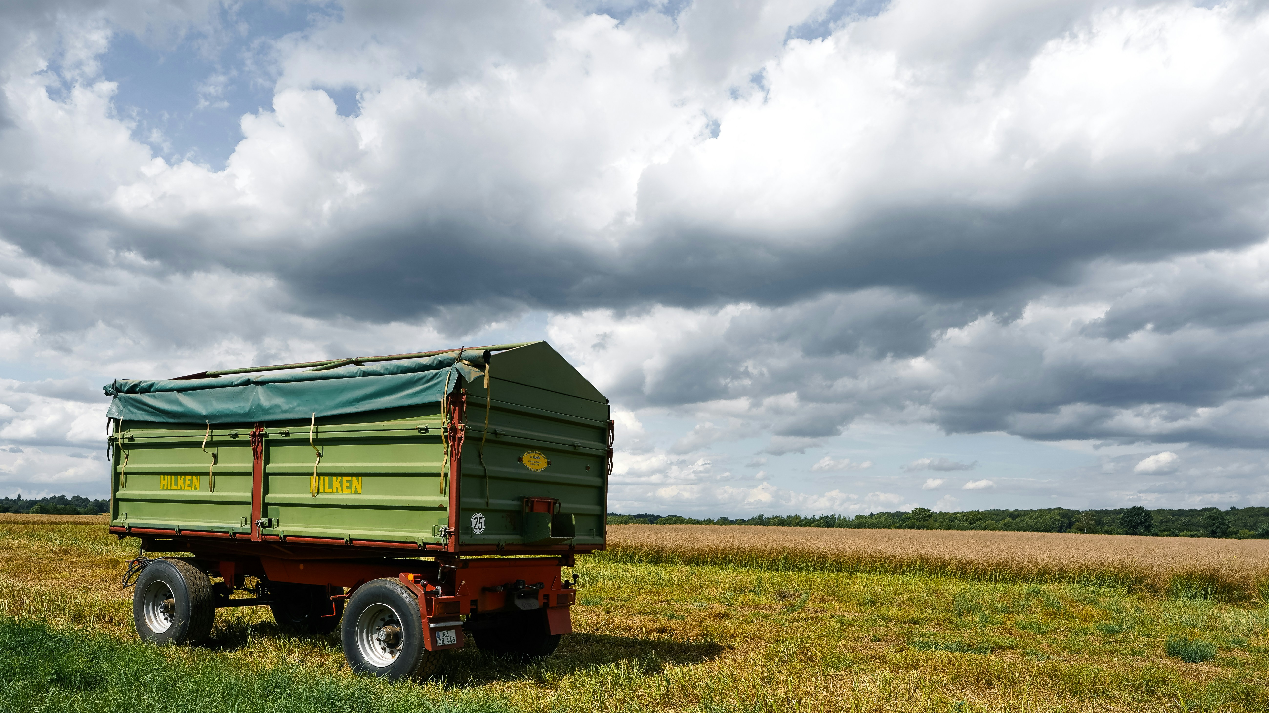 Green trailer in a windswept harvest field under dramatic clouds