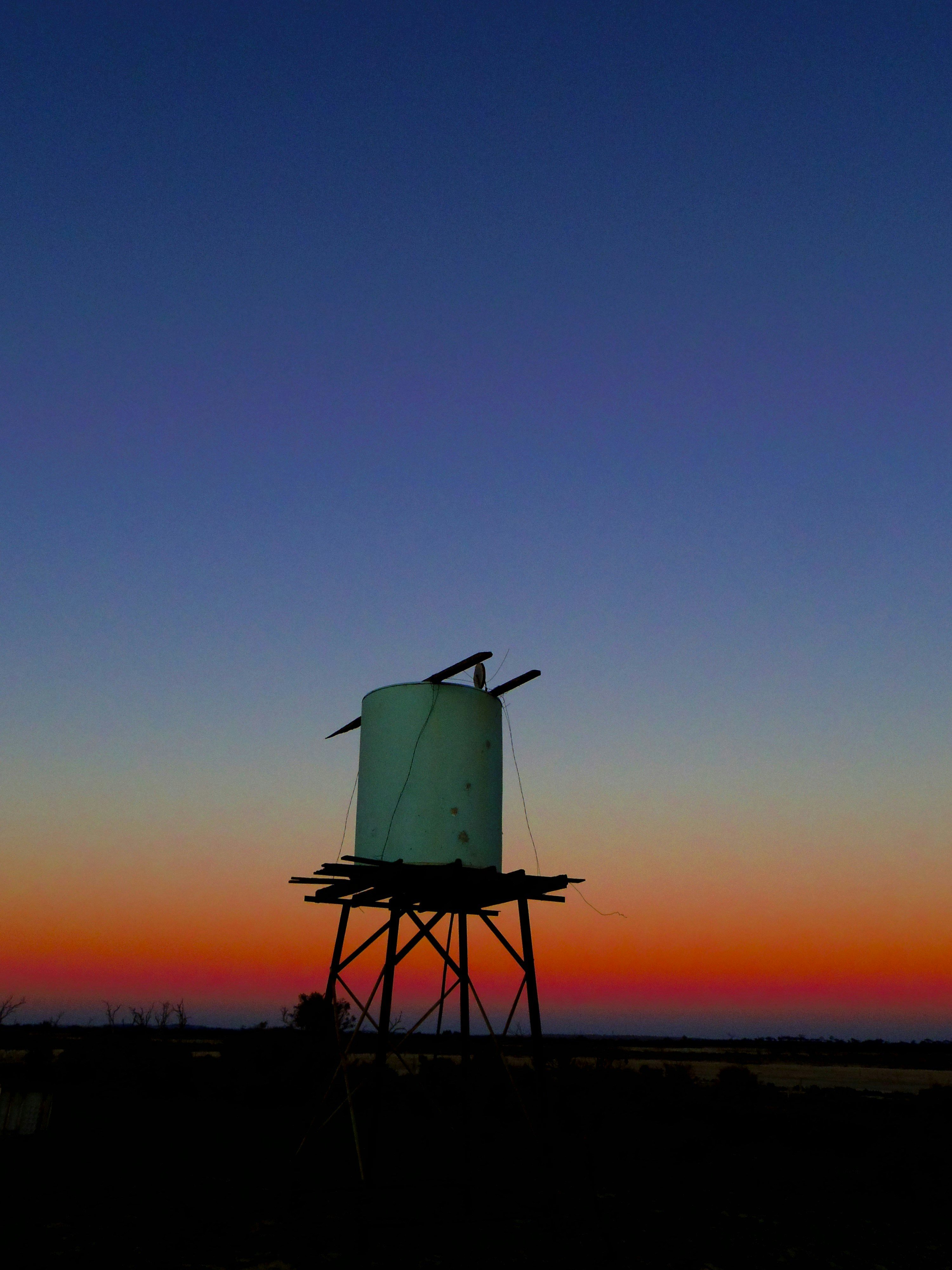 Towering water tank on stilts stands against a dramatic sunset gradient, its silhouette crisp above a flat, dark foreground.
