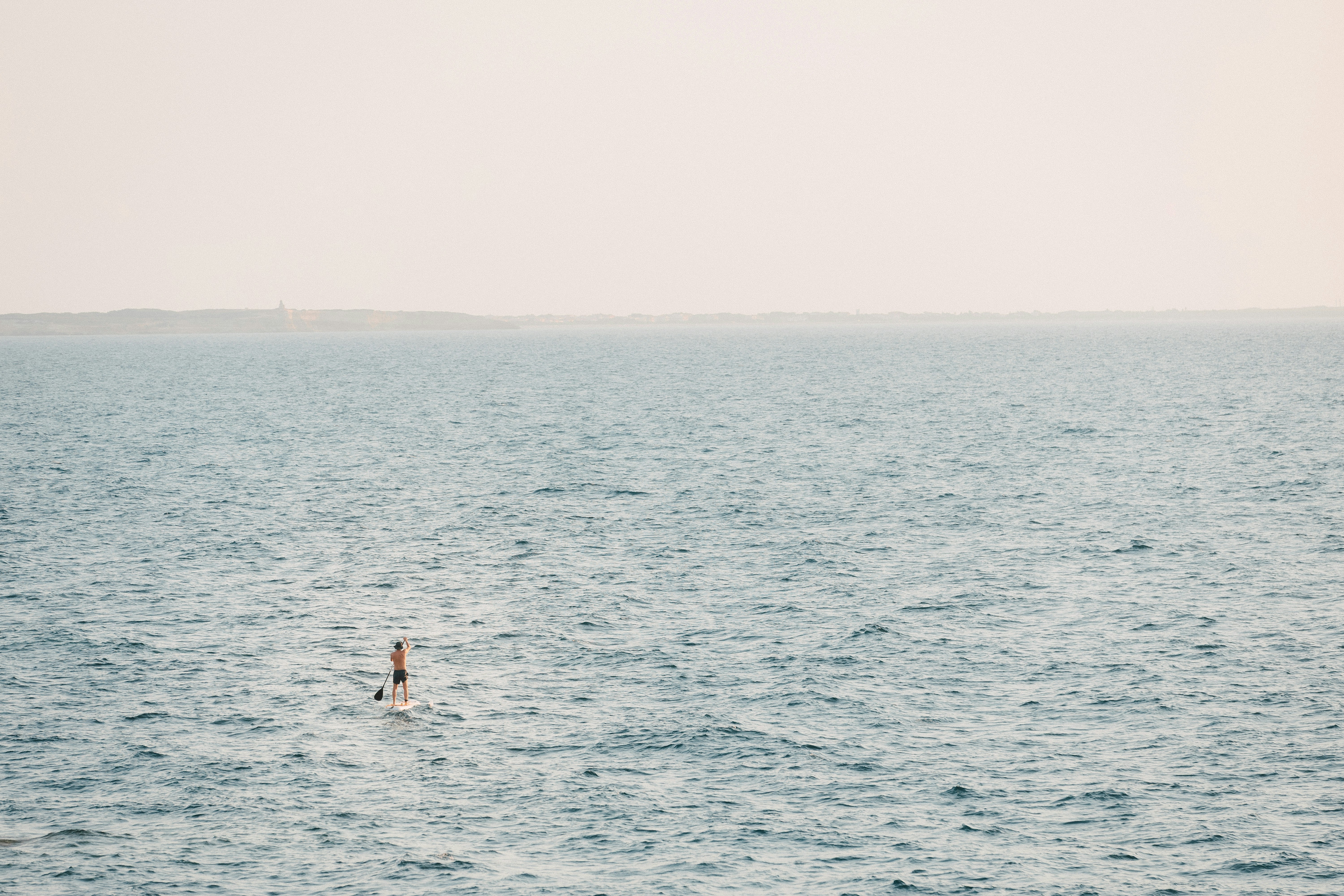  lone paddleboarder carving a quiet line across a hazy sea