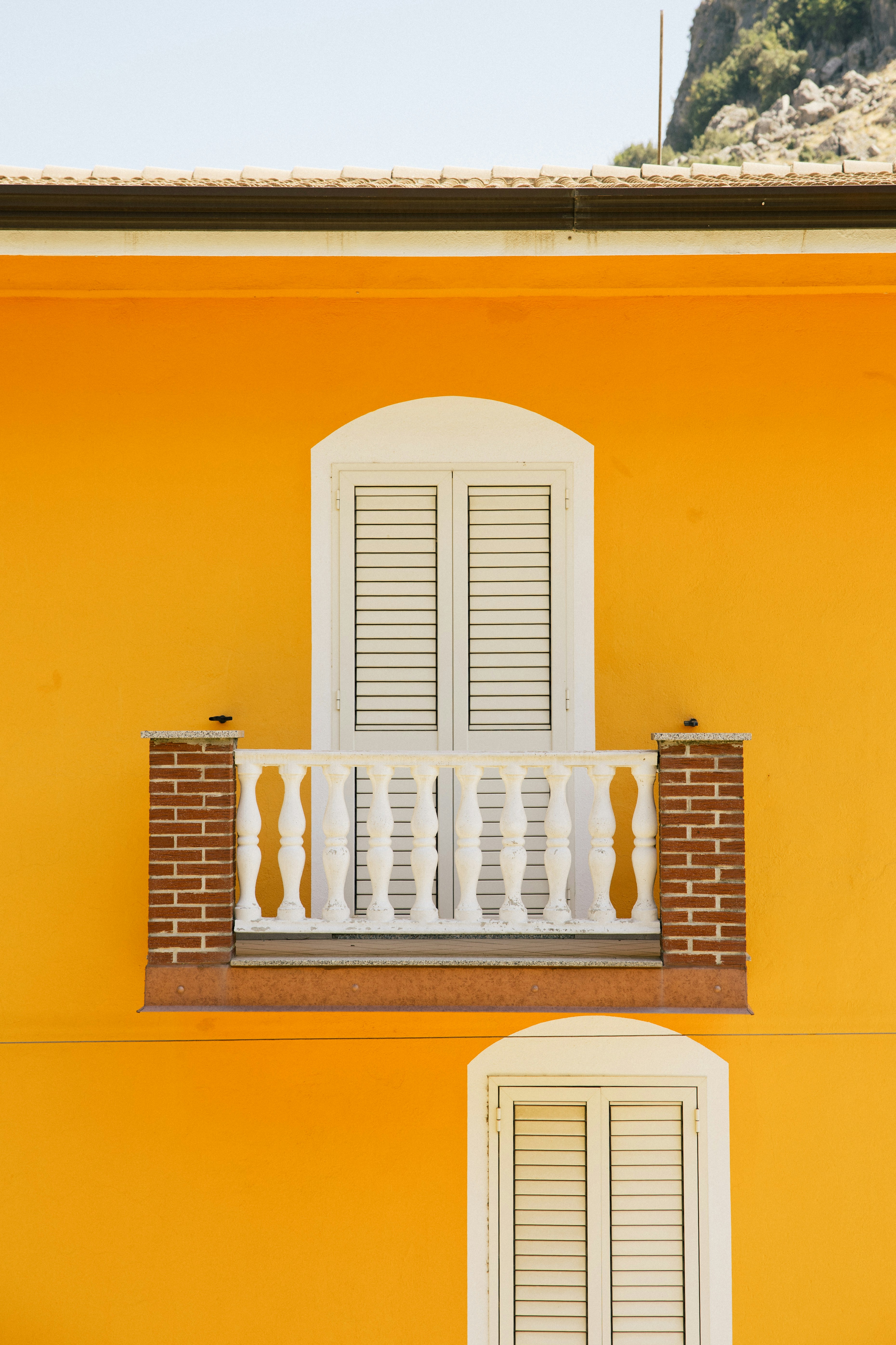 Sunlit Orange Facade with White Balcony and Shuttered Windows