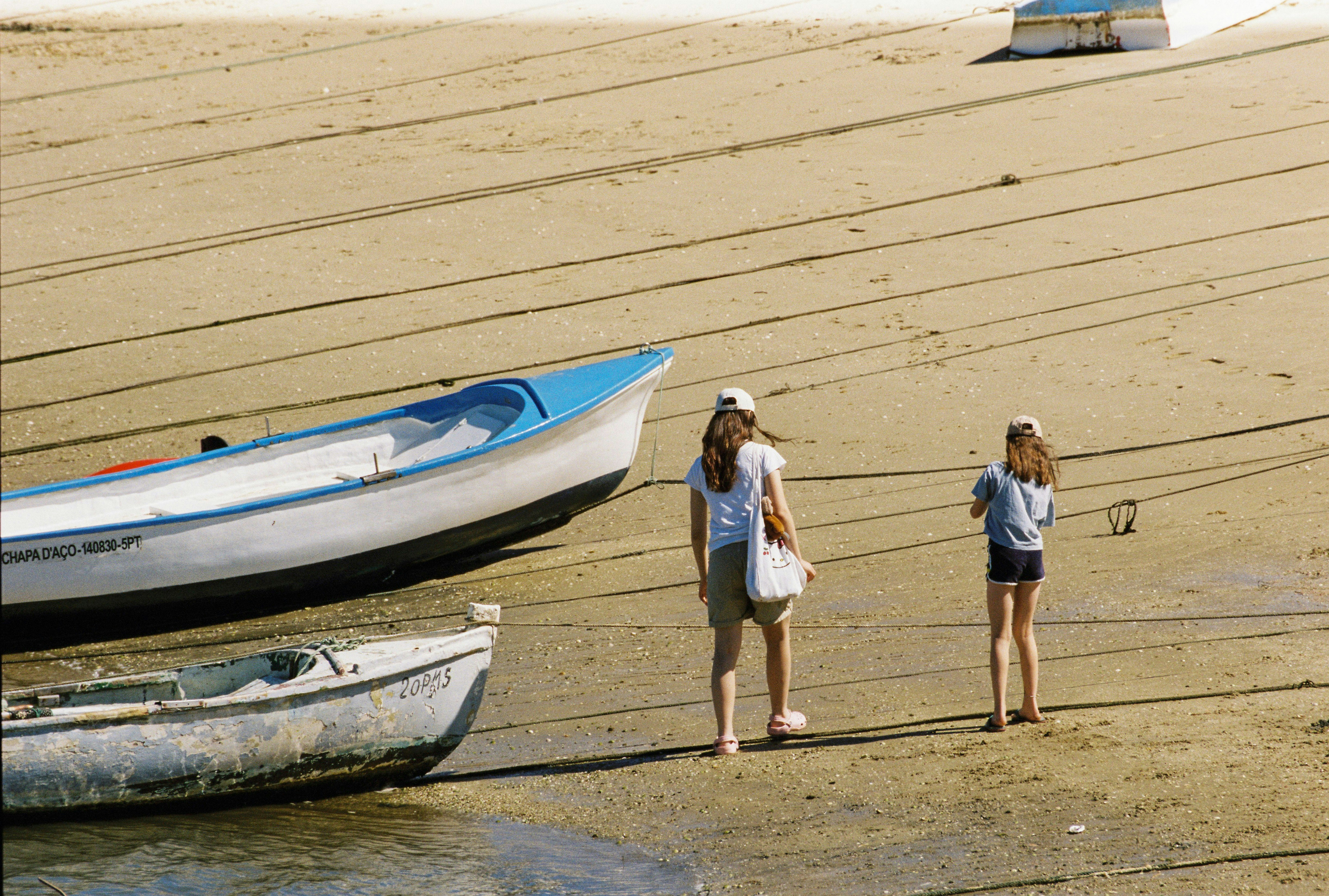 Two Beach Walkers Beneath Tied Boats