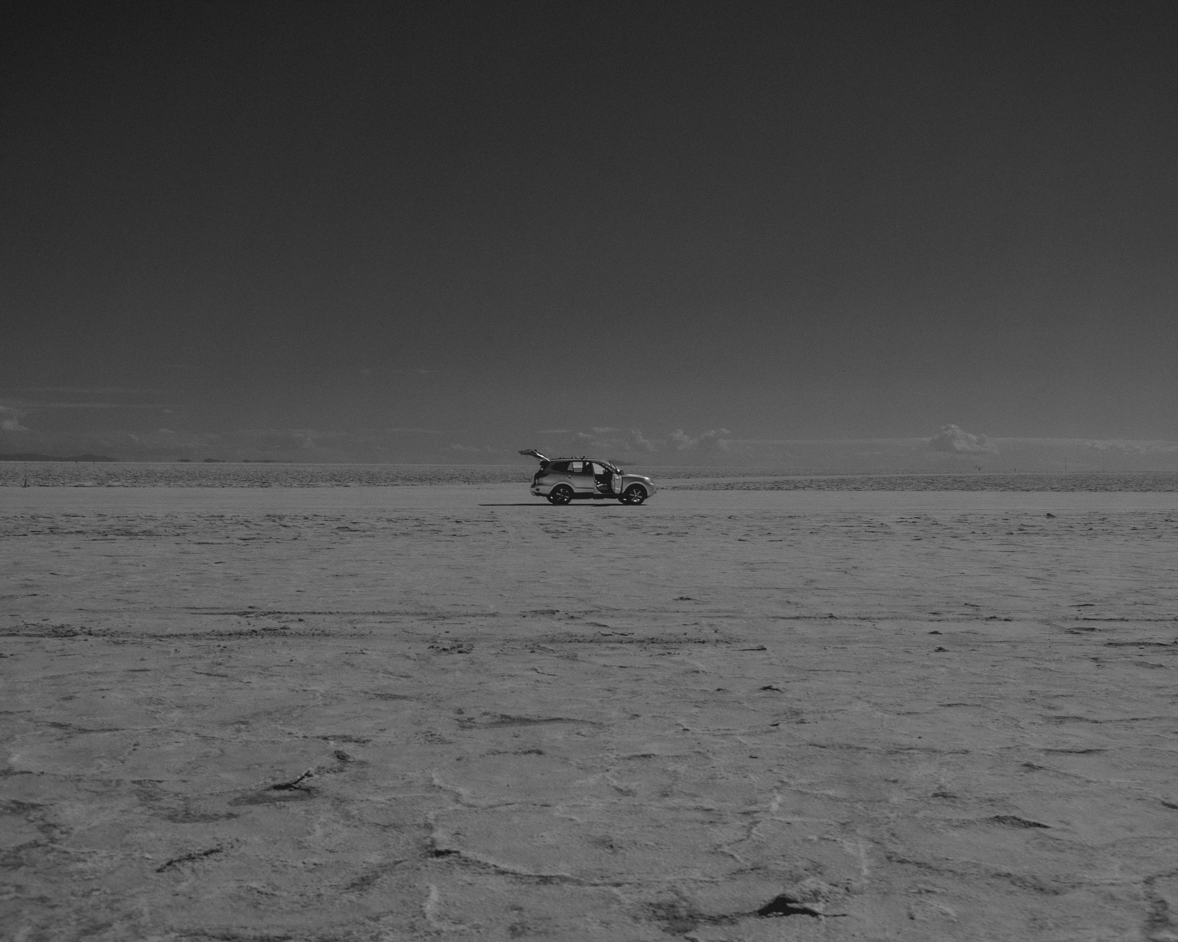 Dusty Expanse: A Lone Vehicle on an Empty Salt Flat