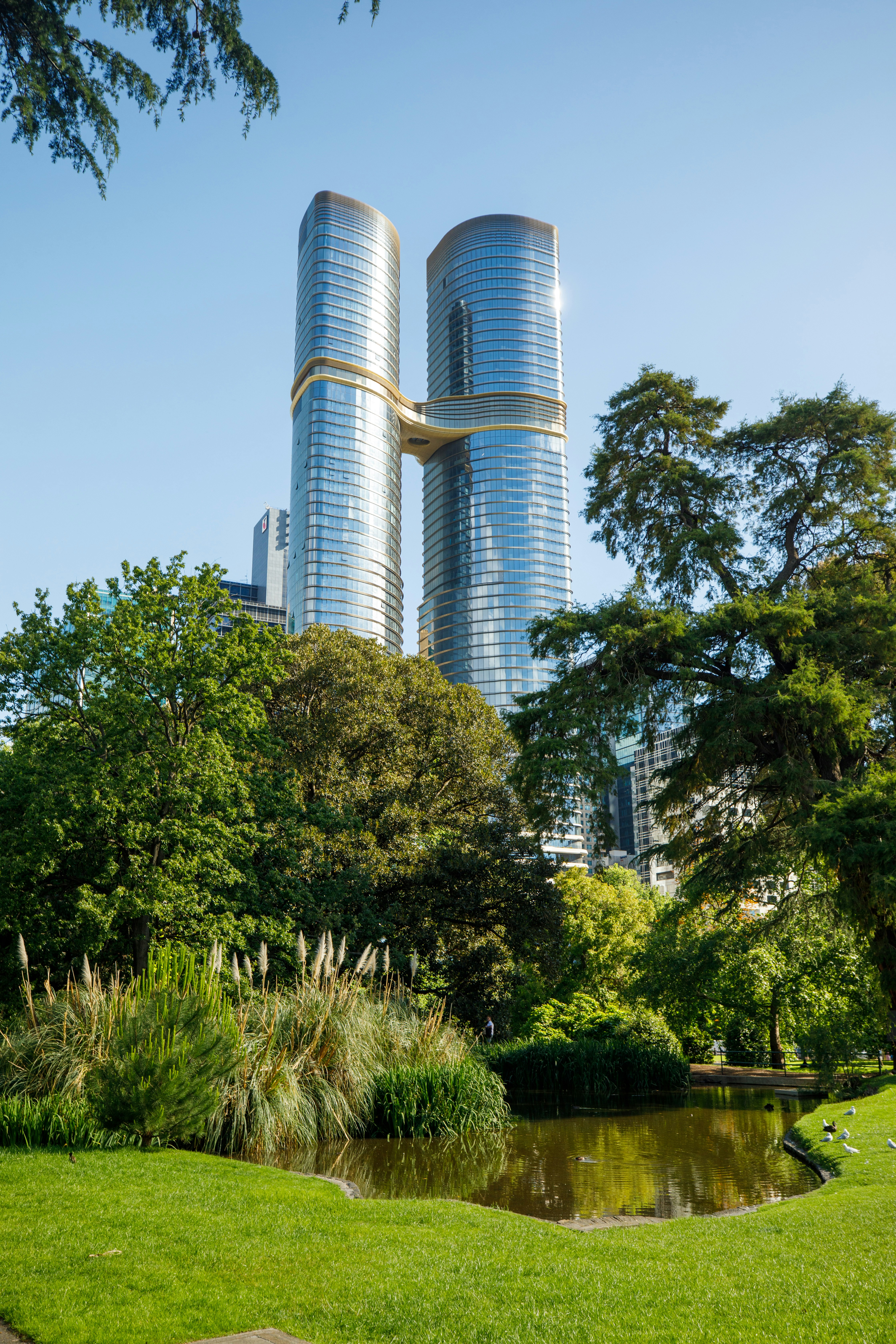 Twin Glass Towers Arched Together Over a Sunlit Park