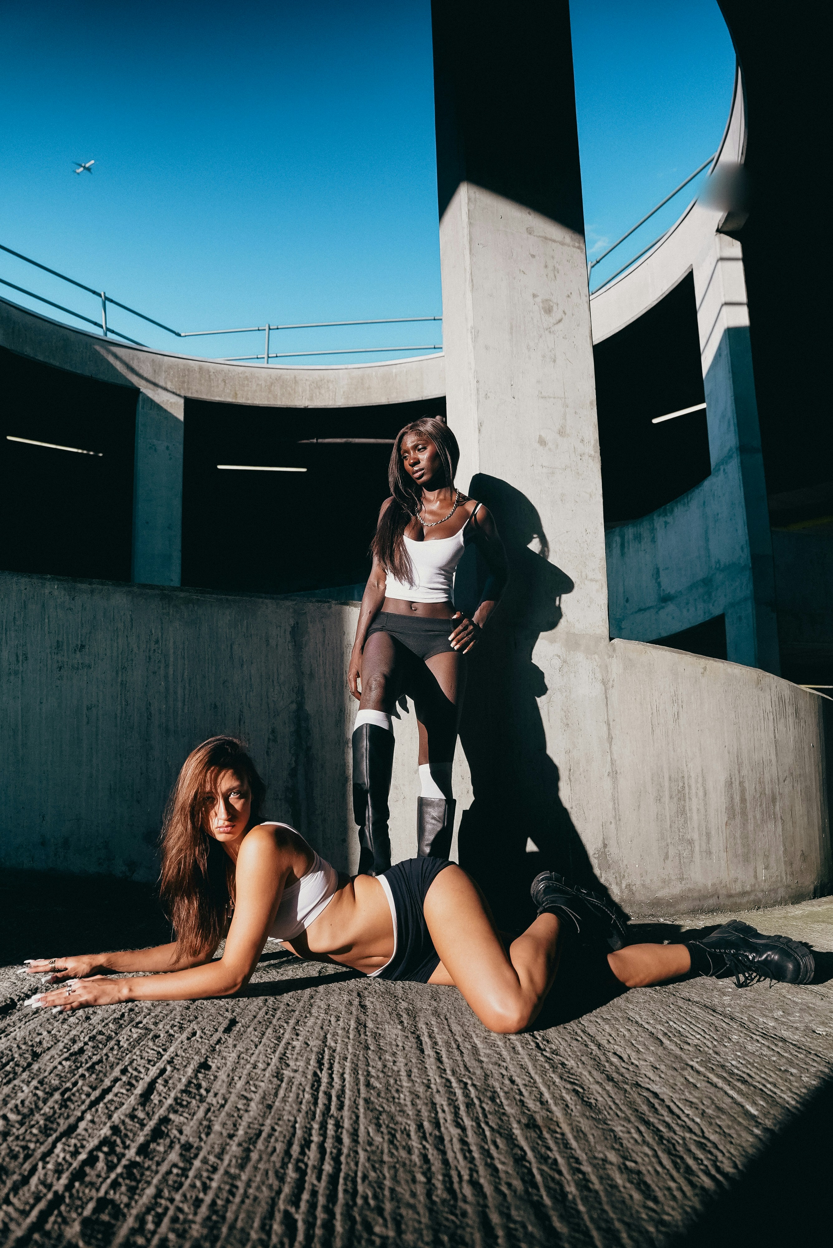 Two-figure strut under brutalist curves: sunlit grit and shadowed confidence