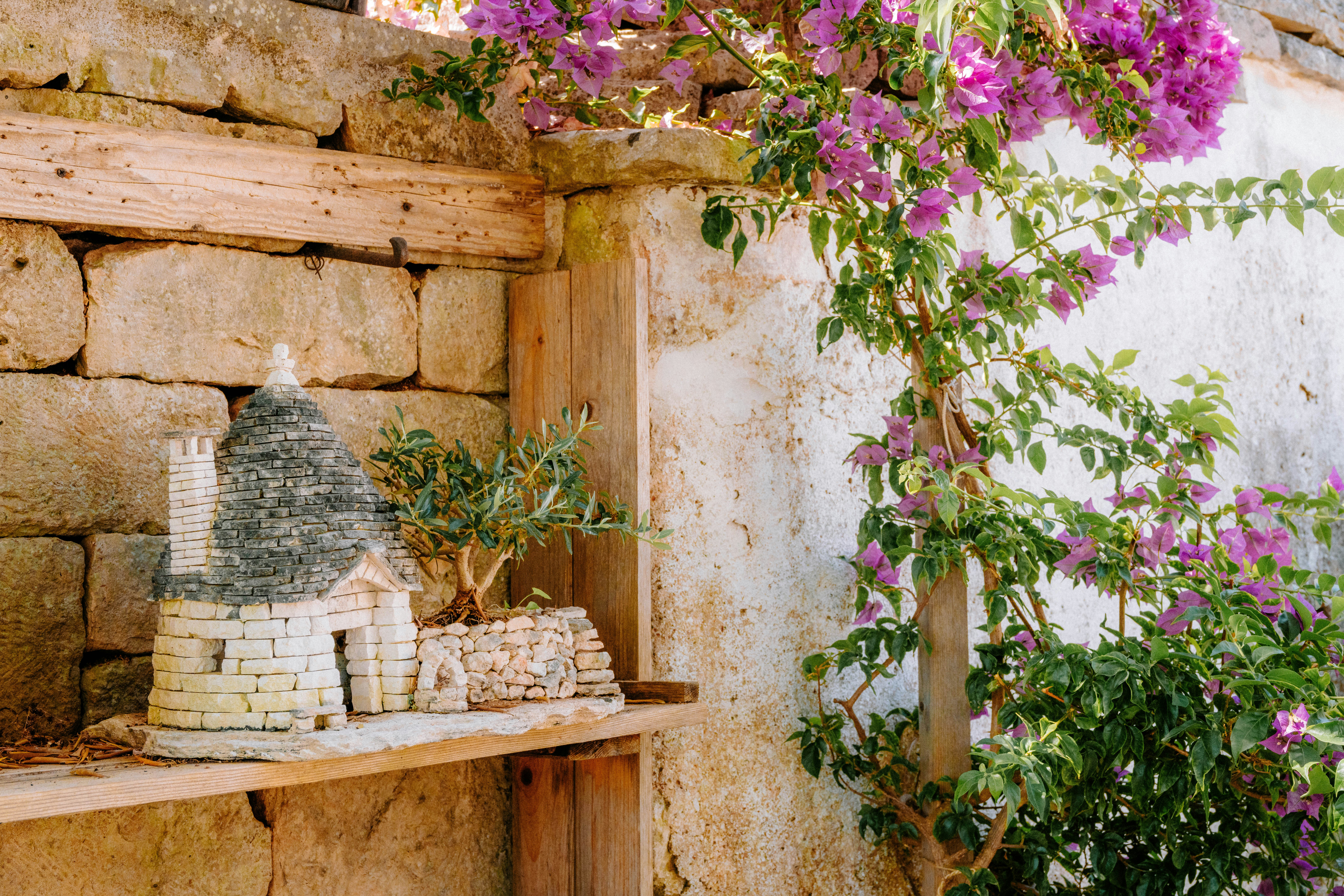Brickwork Shrine: A Tiny Stone House on a Wooden Shelf Surrounded by Bougainvillea