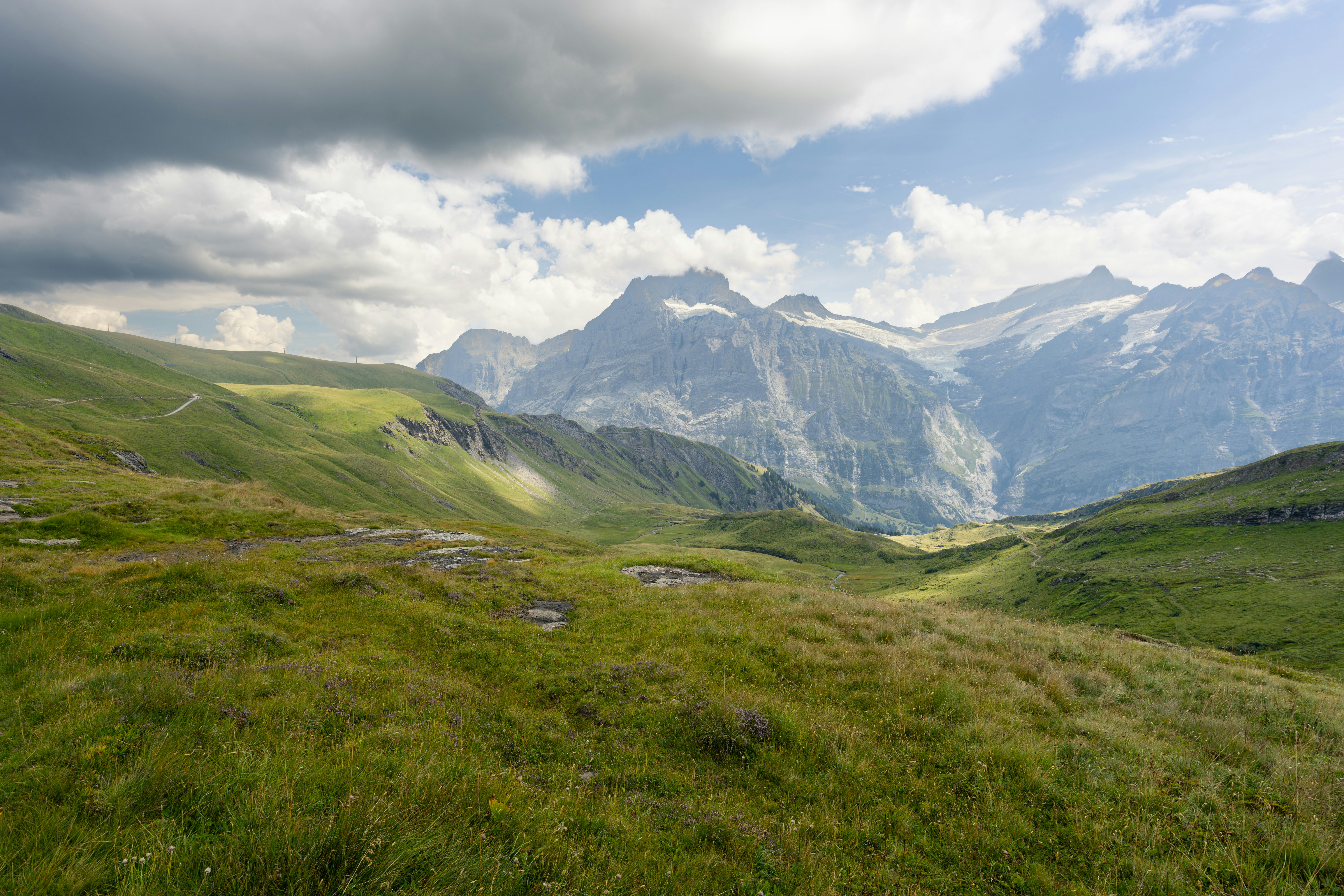 Green mountain slopes leading to a jagged rocky peak under a cloudy sky