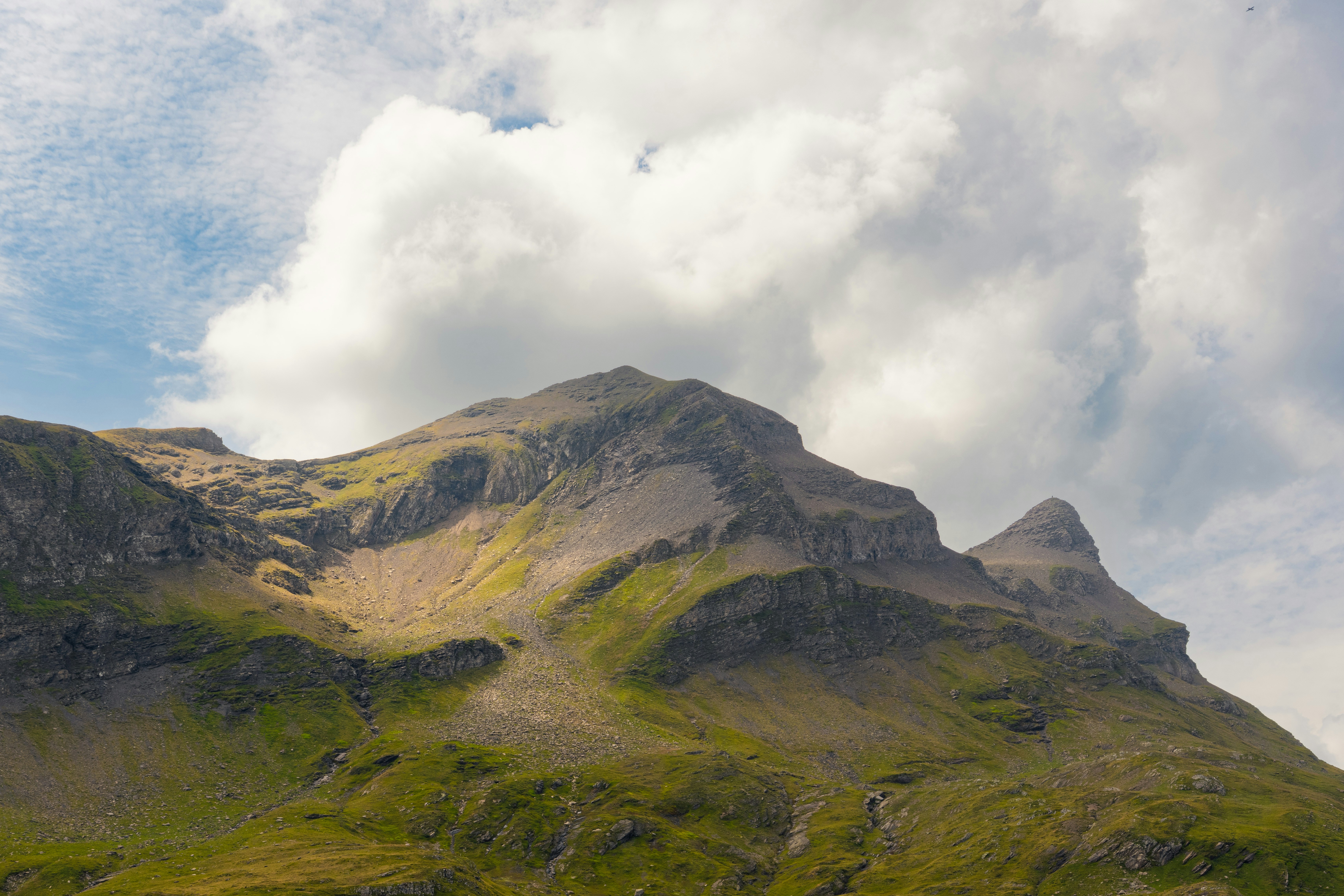 A rocky mountain peak with green slopes under a large white cloud