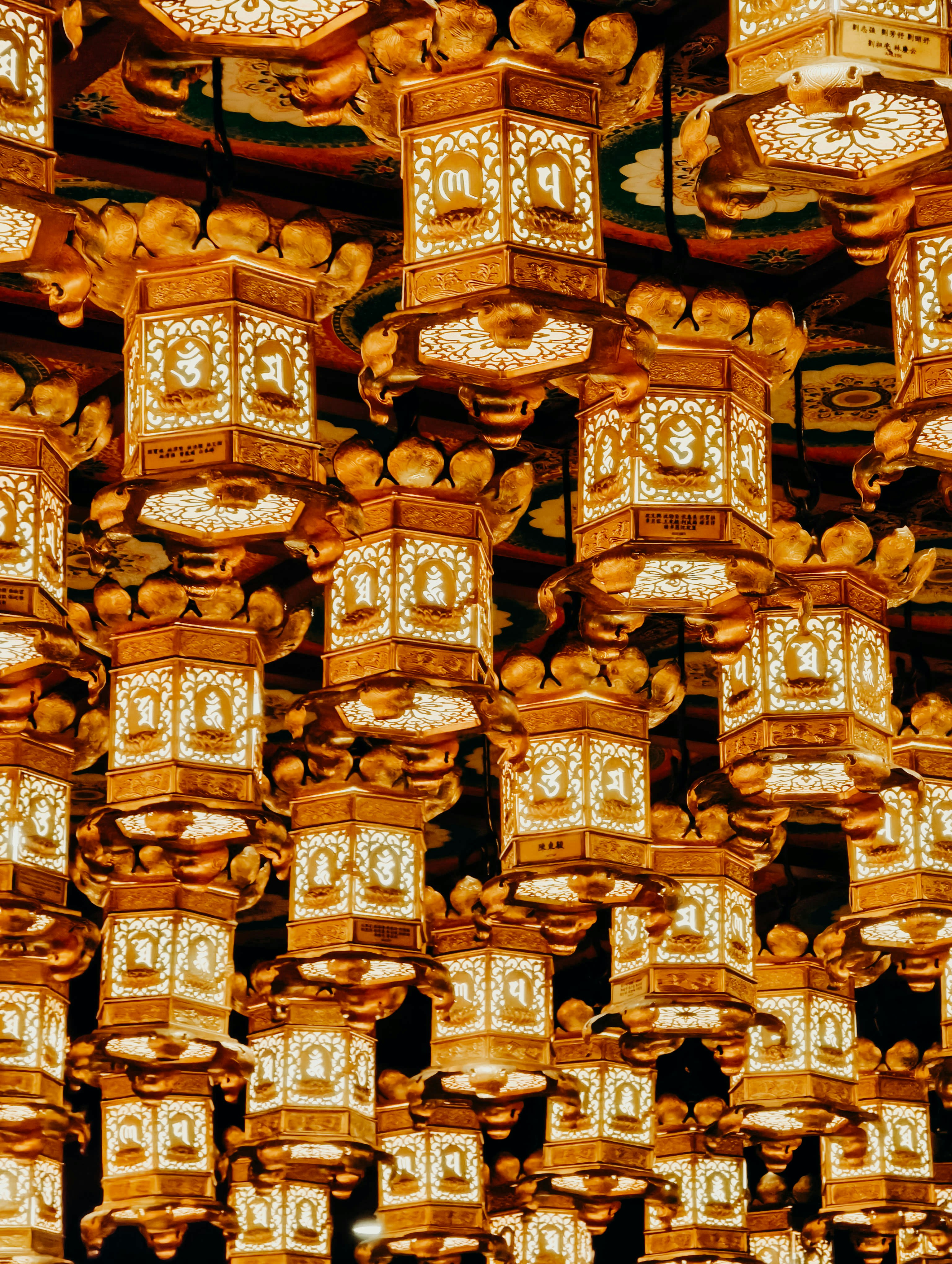 Dense cluster of ornate golden lanterns fills the frame, emitting warm light and intricate patterns. A decorative installation captured as a rich, continuous texture.