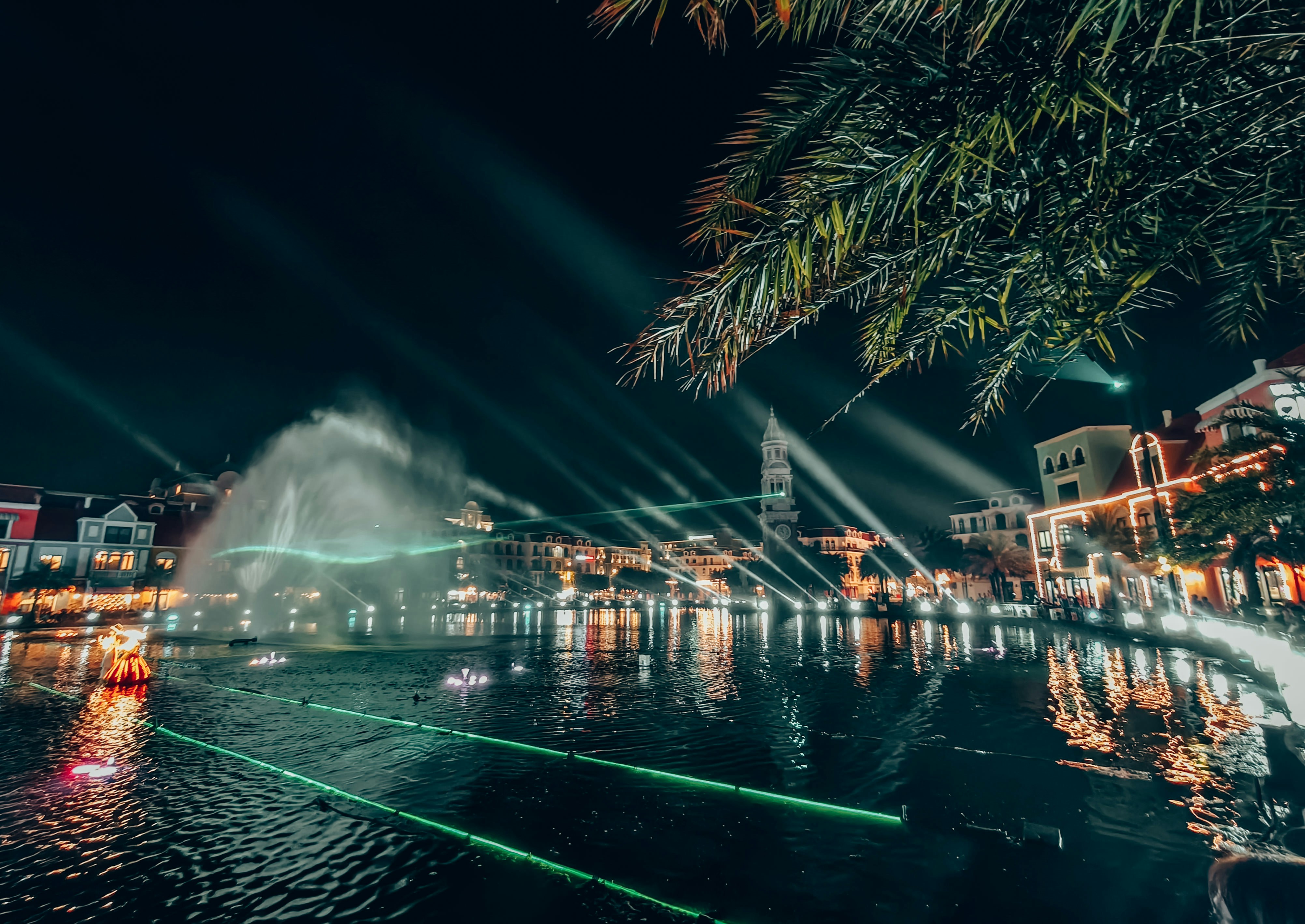 Night Canal Fountains Under Neon Pines and Town Lights
