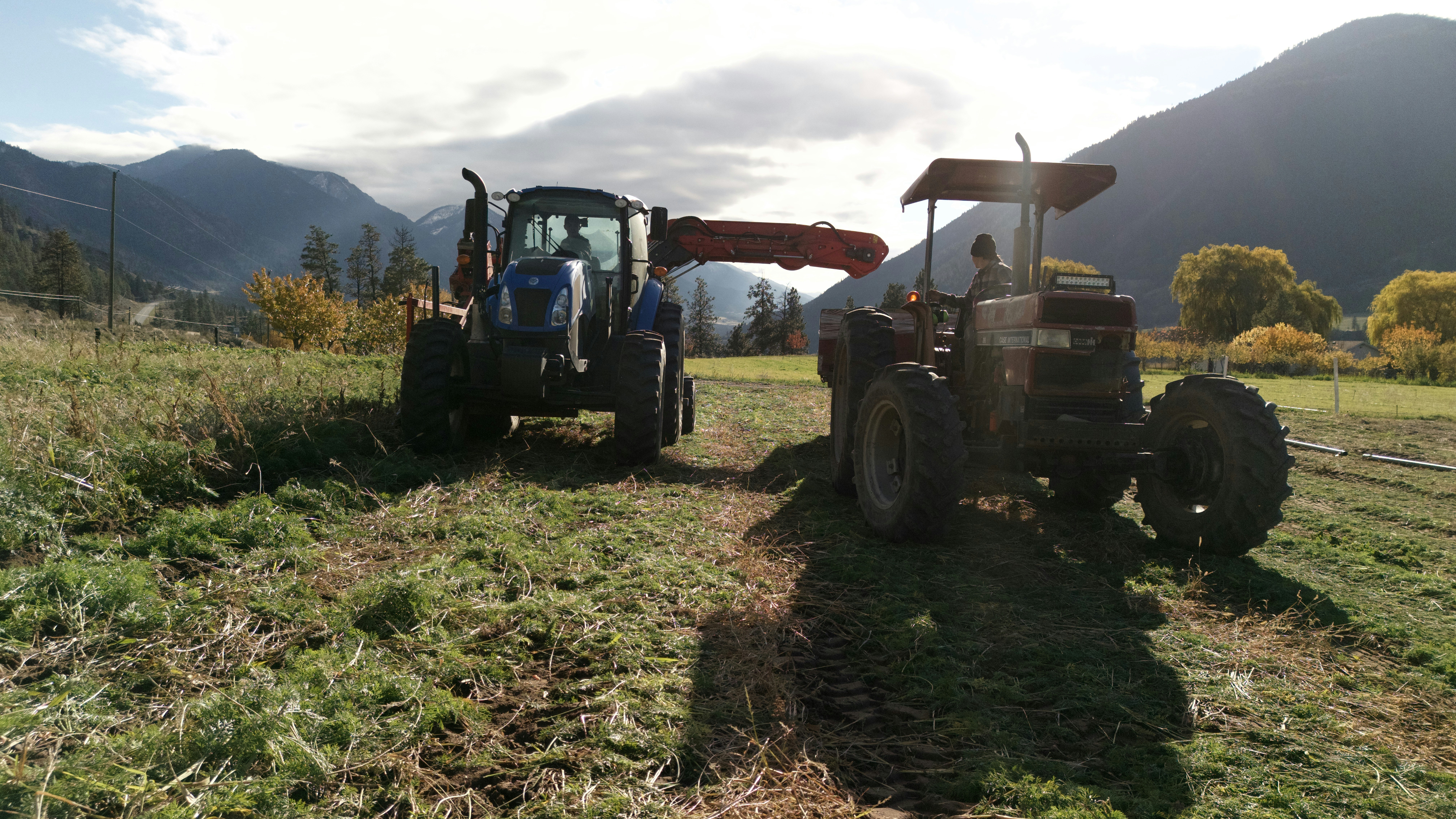 Two tractors rest on a sunlit field as distant mountains frame the scene