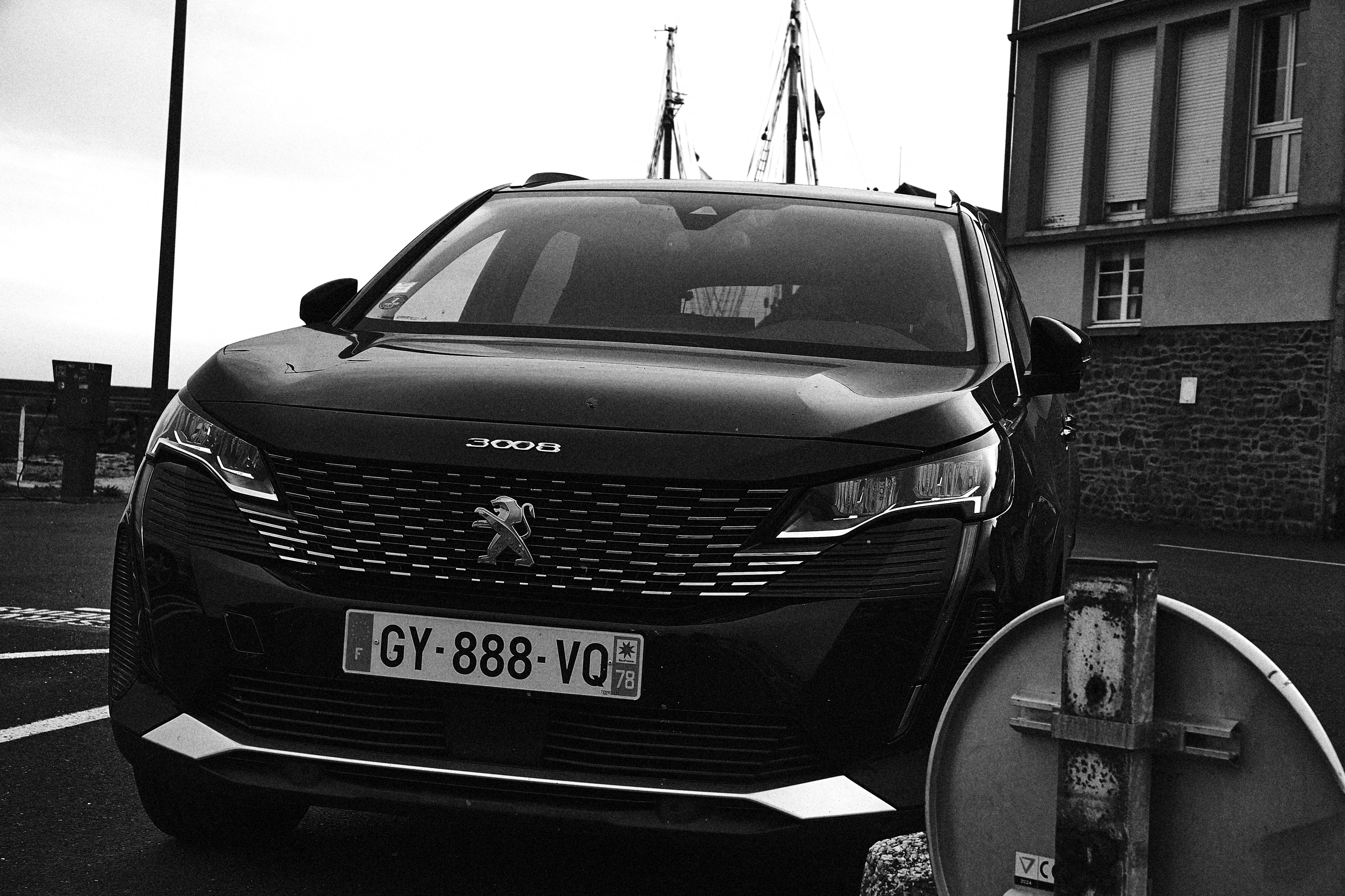 黑白街景中，一辆 Peugeot 3008 正面近景置于画面左侧，车牌清晰，背景为港口与建筑物。画面强调车辆设计与纹理细节。