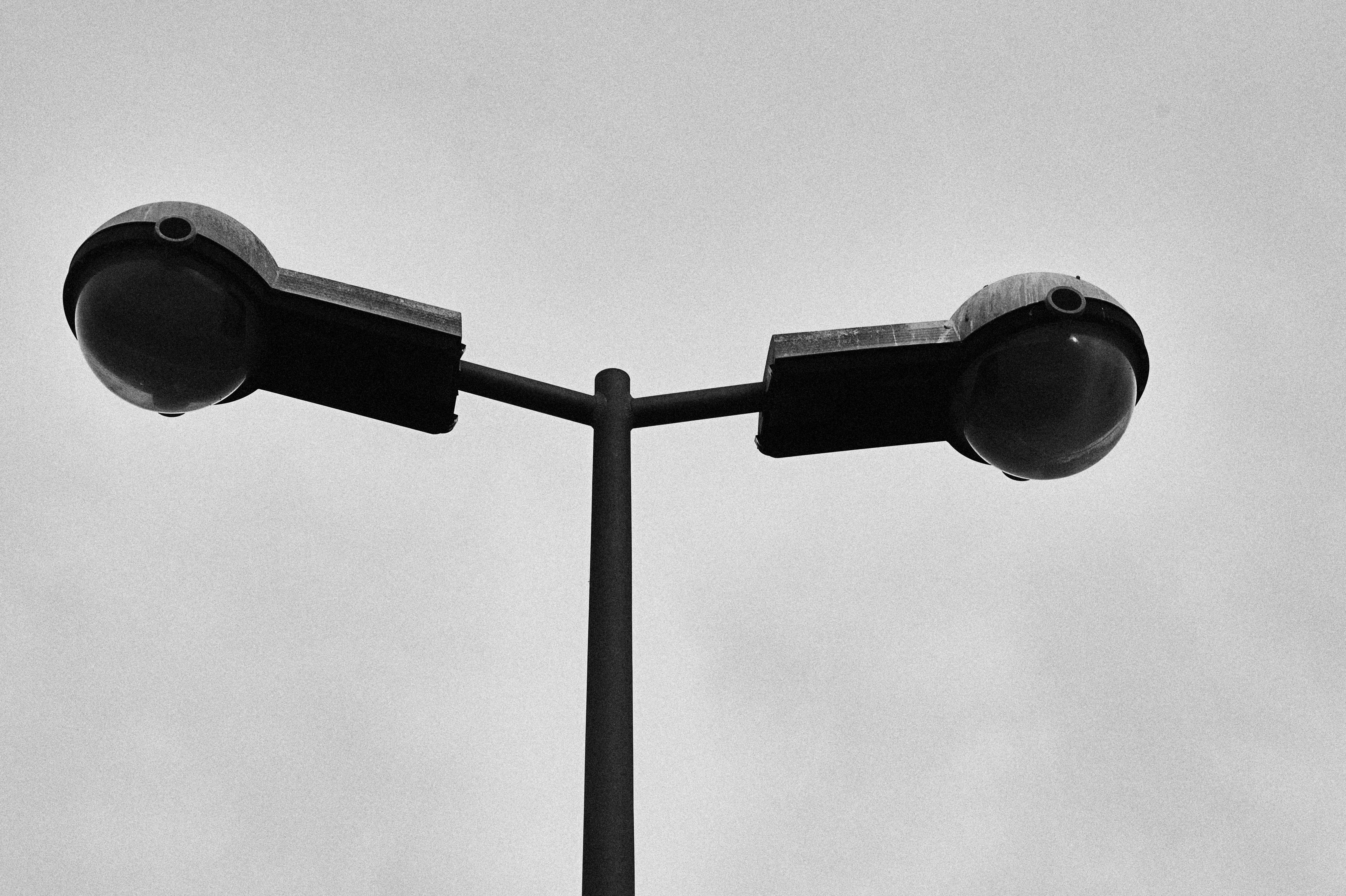 Minimalist black-and-white image of a two-headed streetlamp against an open sky, emphasizing symmetry and stark contrast.