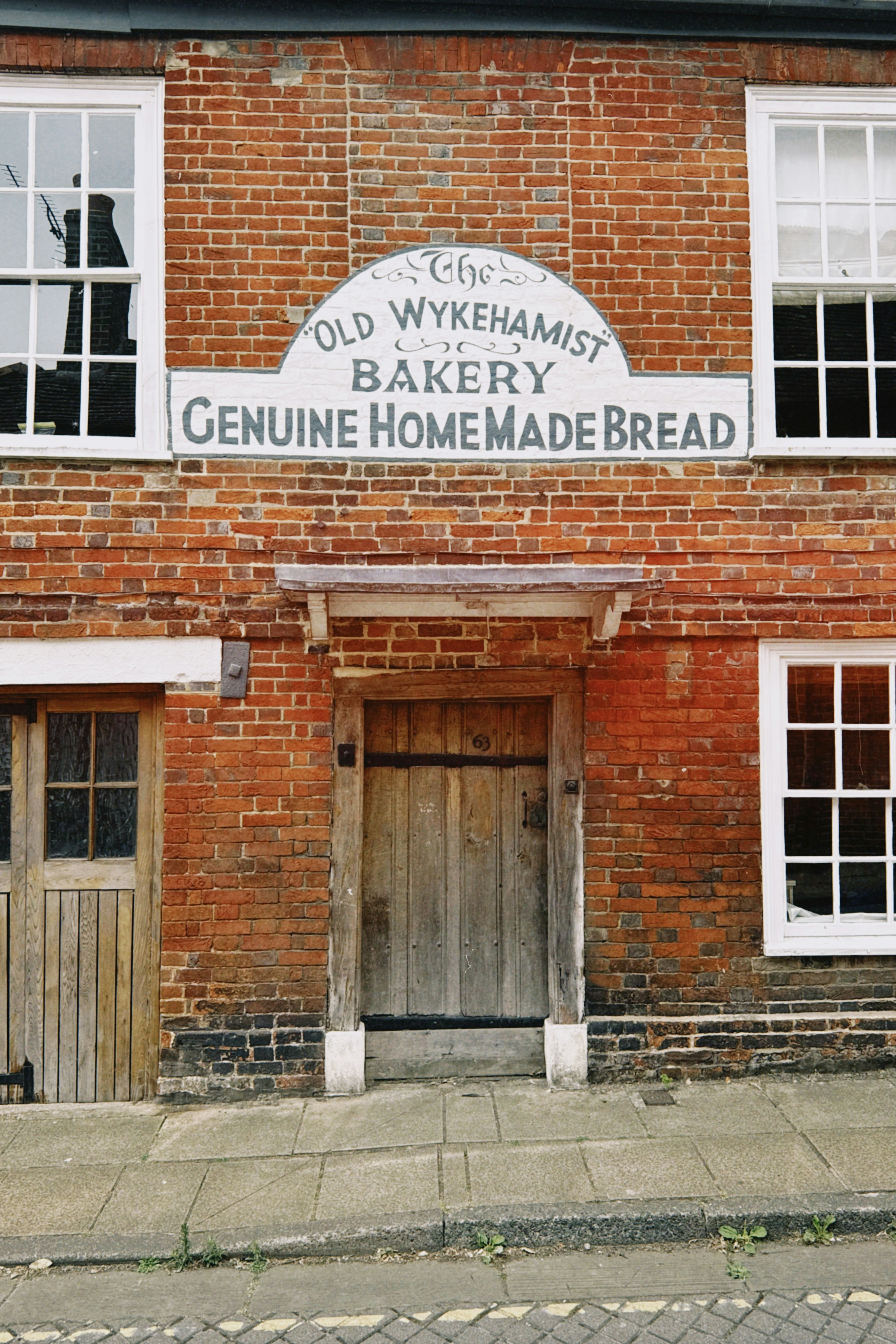 A brick building with a sign reading The Old Wykehamist Bakery above a wooden door